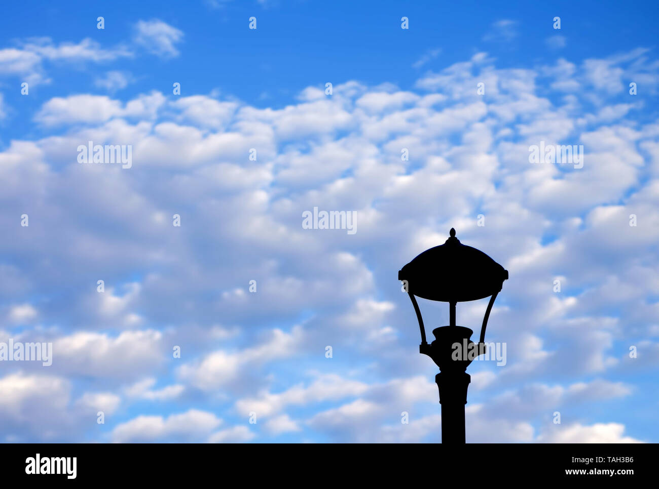Silhouette of a street lamp missing a bulb among a bright cloudy day ...