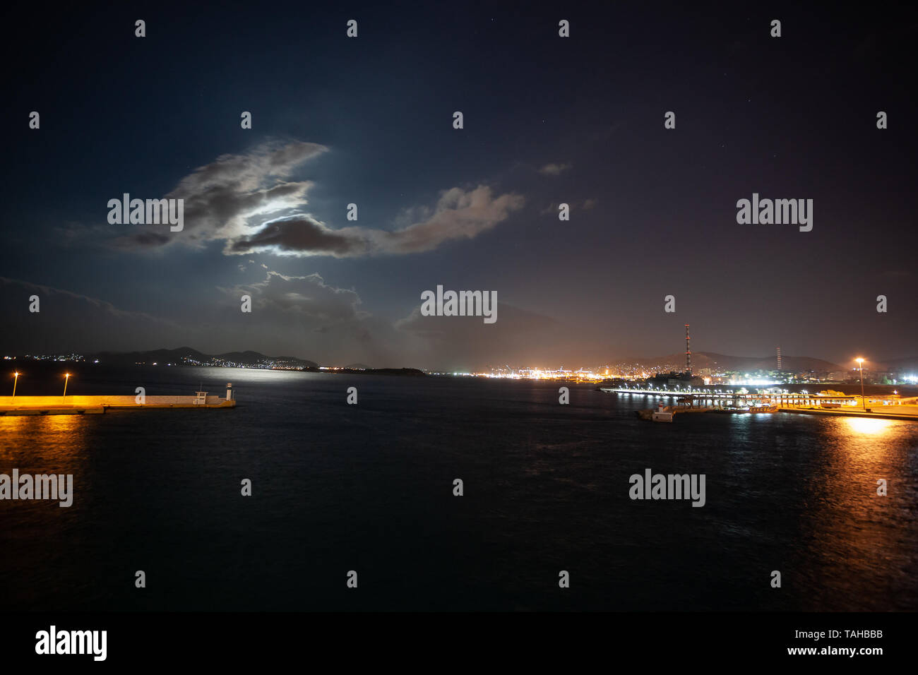 Night view of Athens Piraeus harbor with moon partially hidden by ...