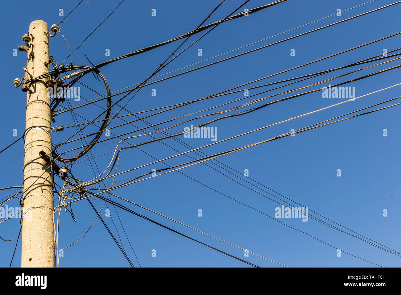 Power pole with intertwined wires against blue sky Stock Photo - Alamy
