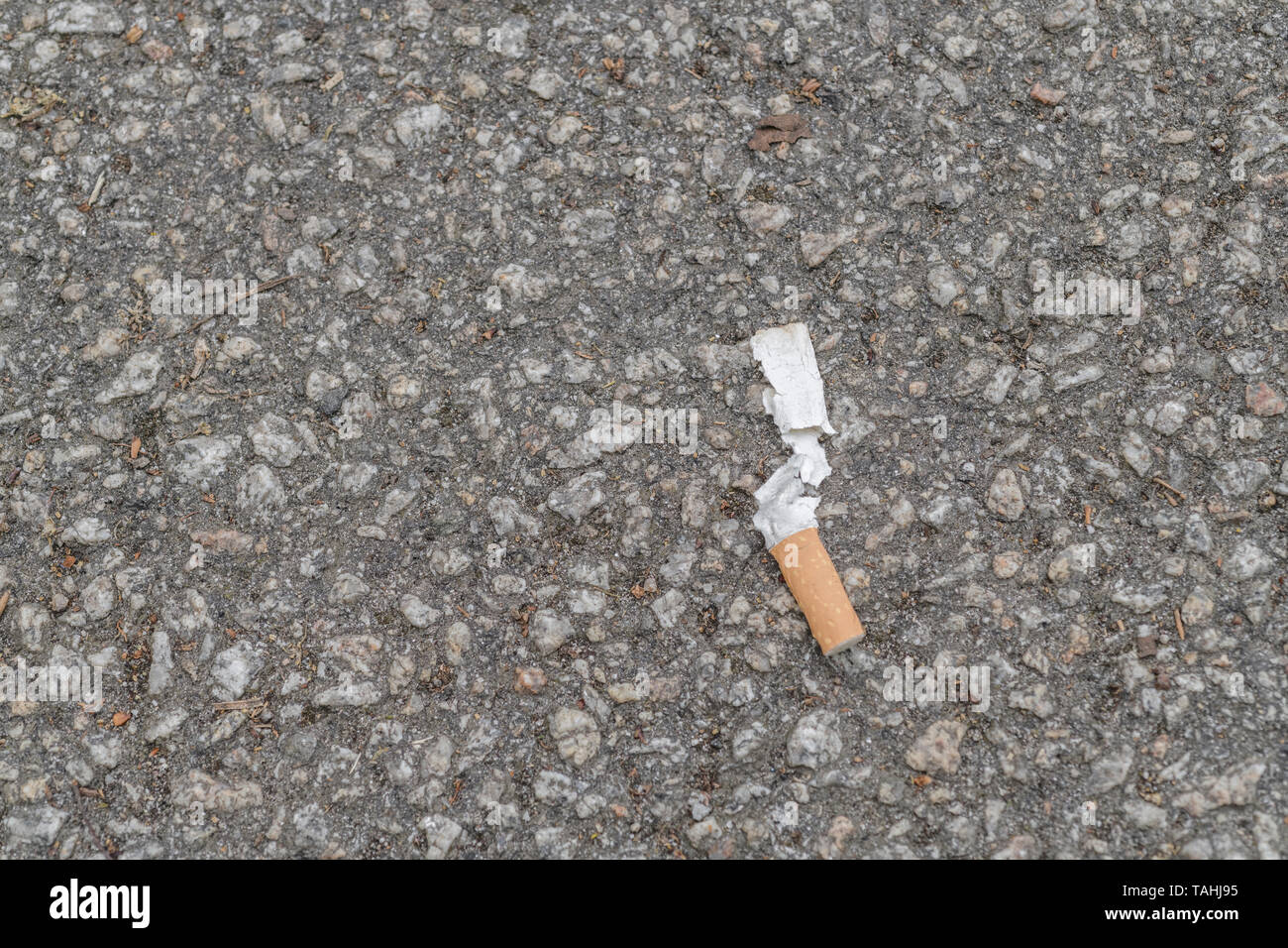 Stubbed out cigarette end on tarmac surface - giving up smoking concept ...