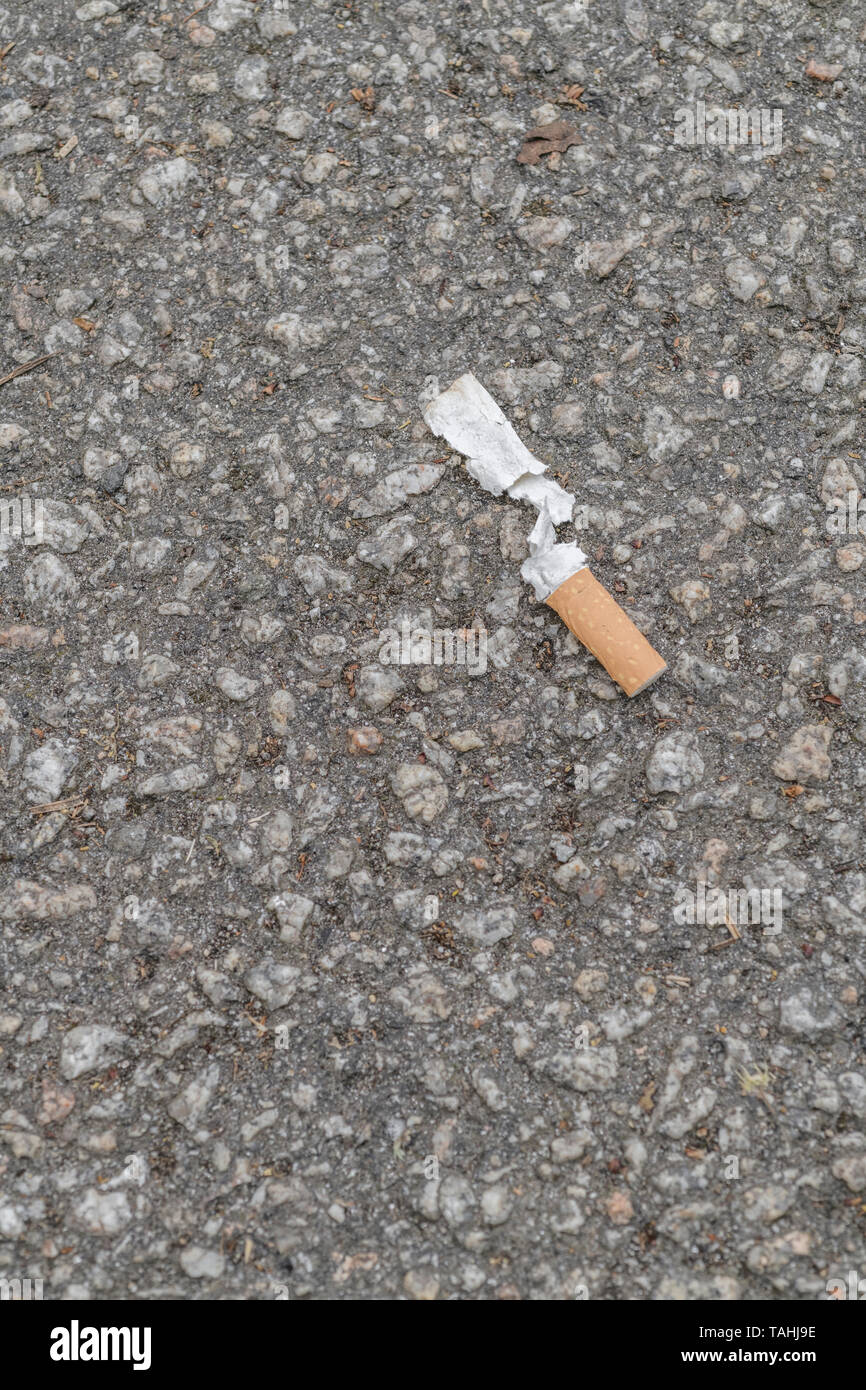 Stubbed out cigarette end on tarmac surface - giving up smoking concept ...