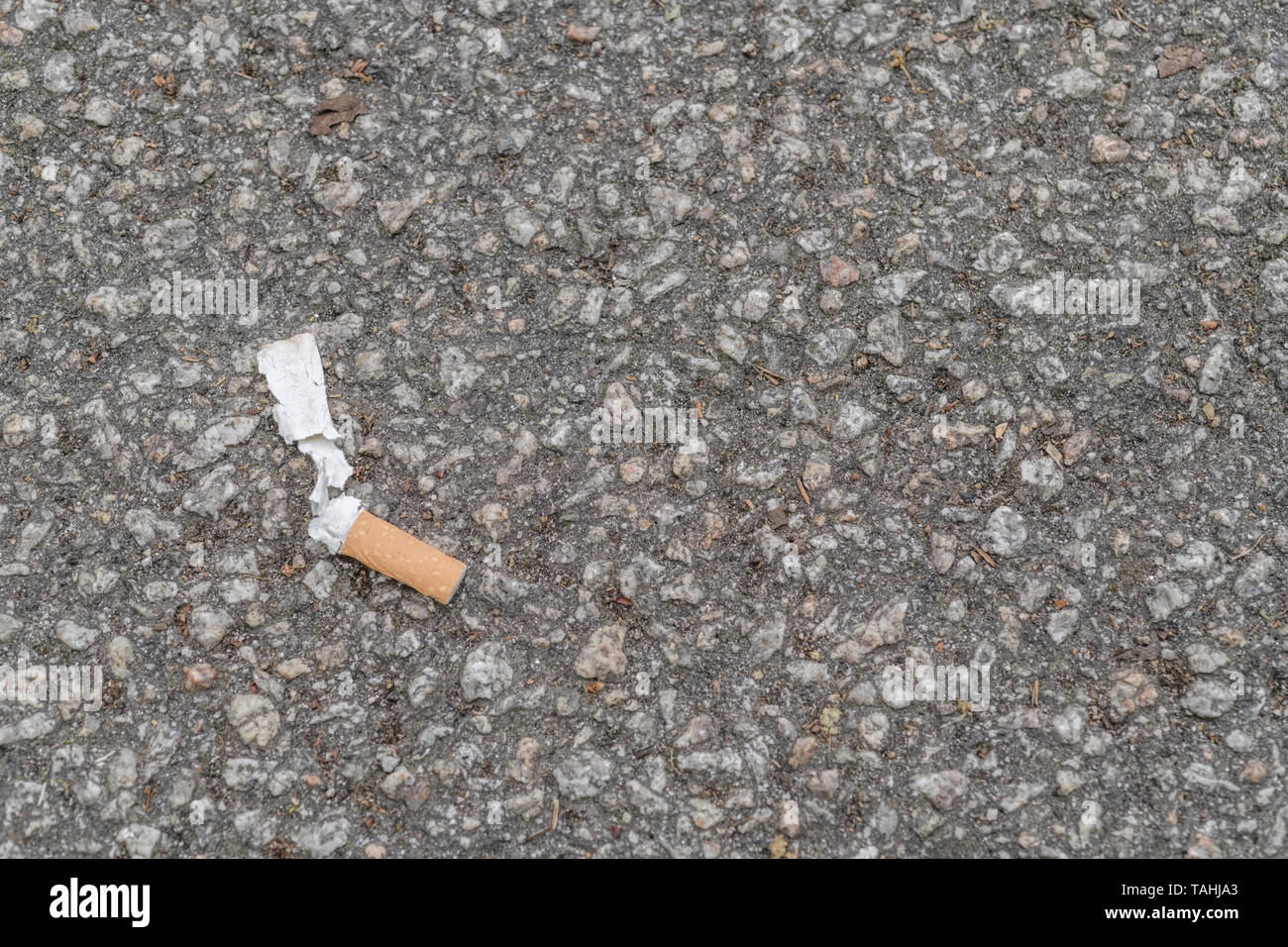 Stubbed out cigarette end on tarmac surface - giving up smoking concept ...