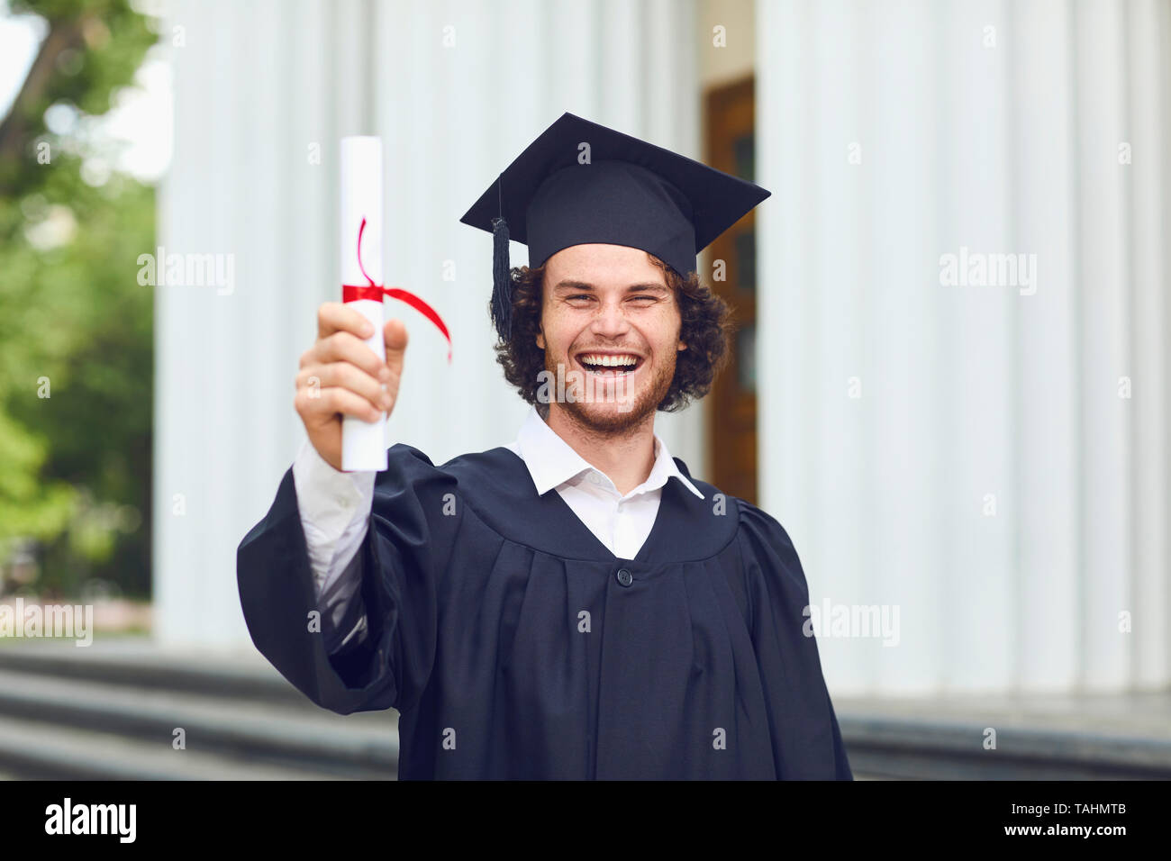 A young man graduate with a scroll in his hands is smiling against the ...