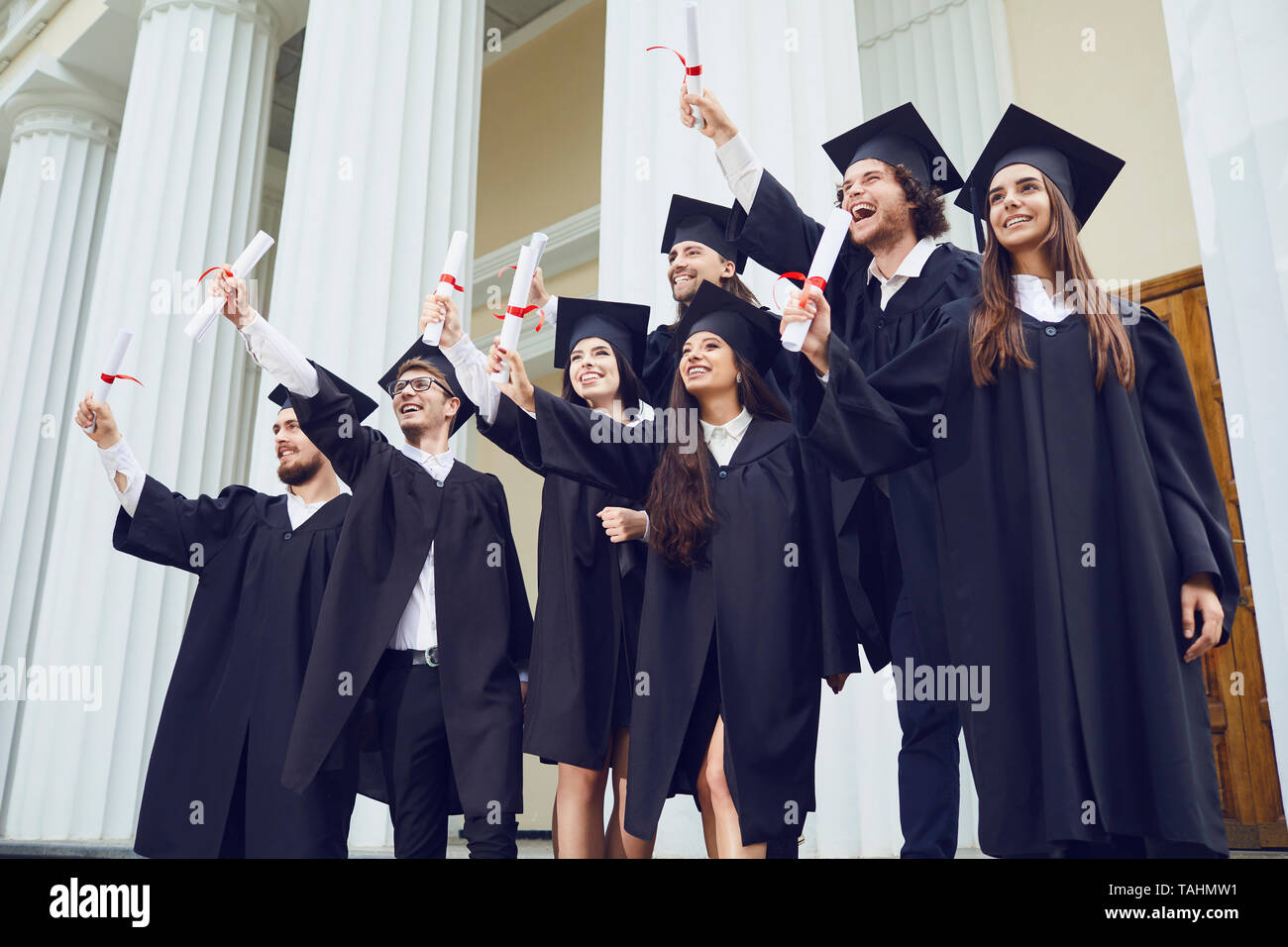 A group of young graduate students raised their hands with diplomas up ...