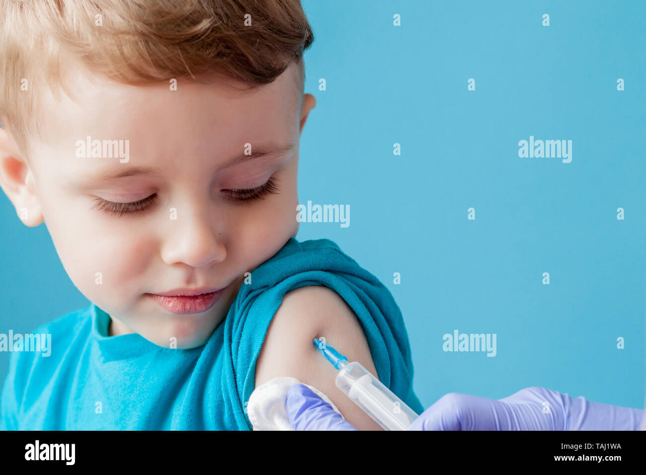Vaccination concept. Female doctor vaccinating cute little boy on blue ...