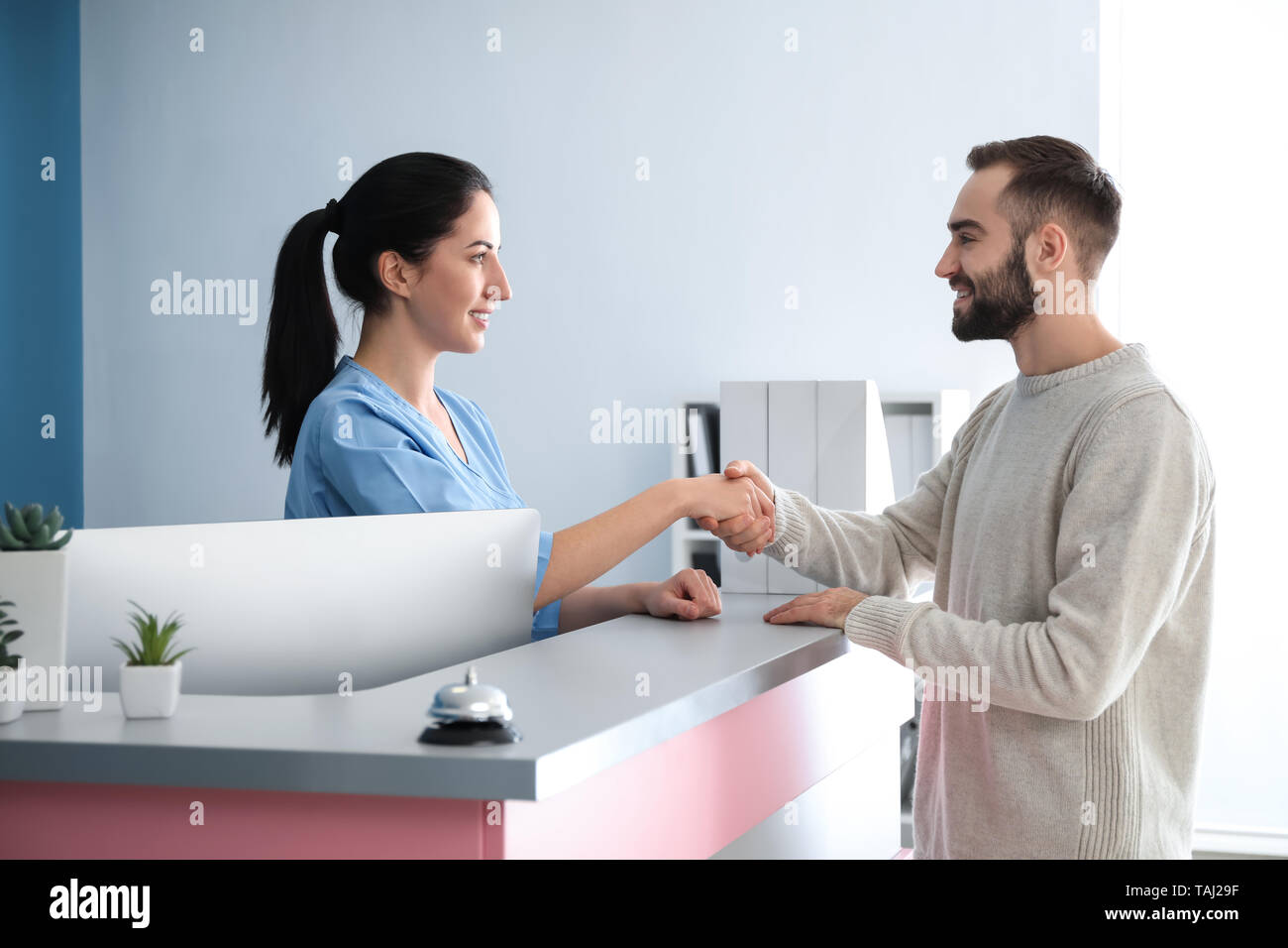 Young man and female receptionist shaking hands in clinic Stock Photo ...