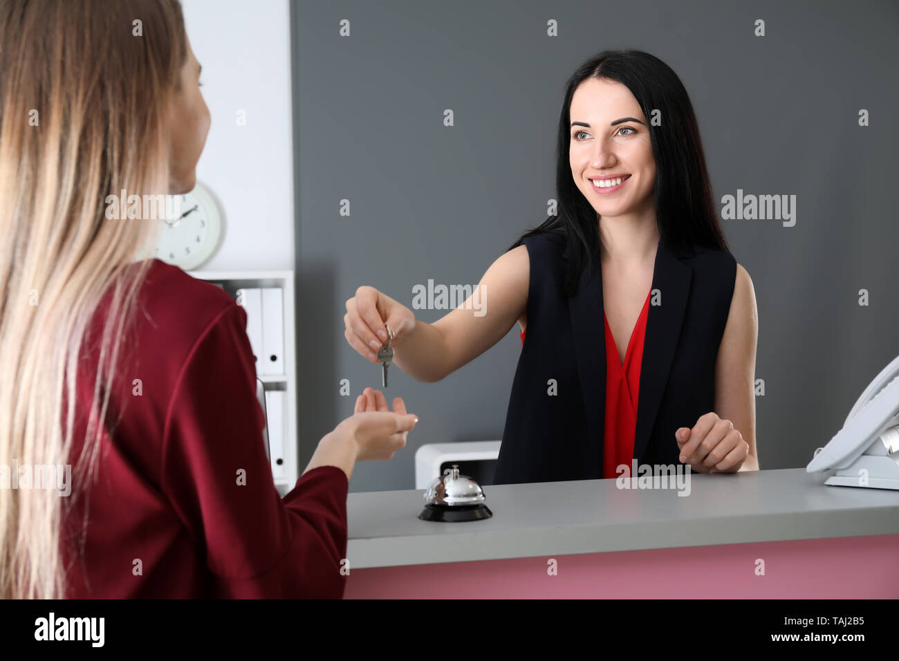 Young woman receiving key from her room at reception desk in hotel ...