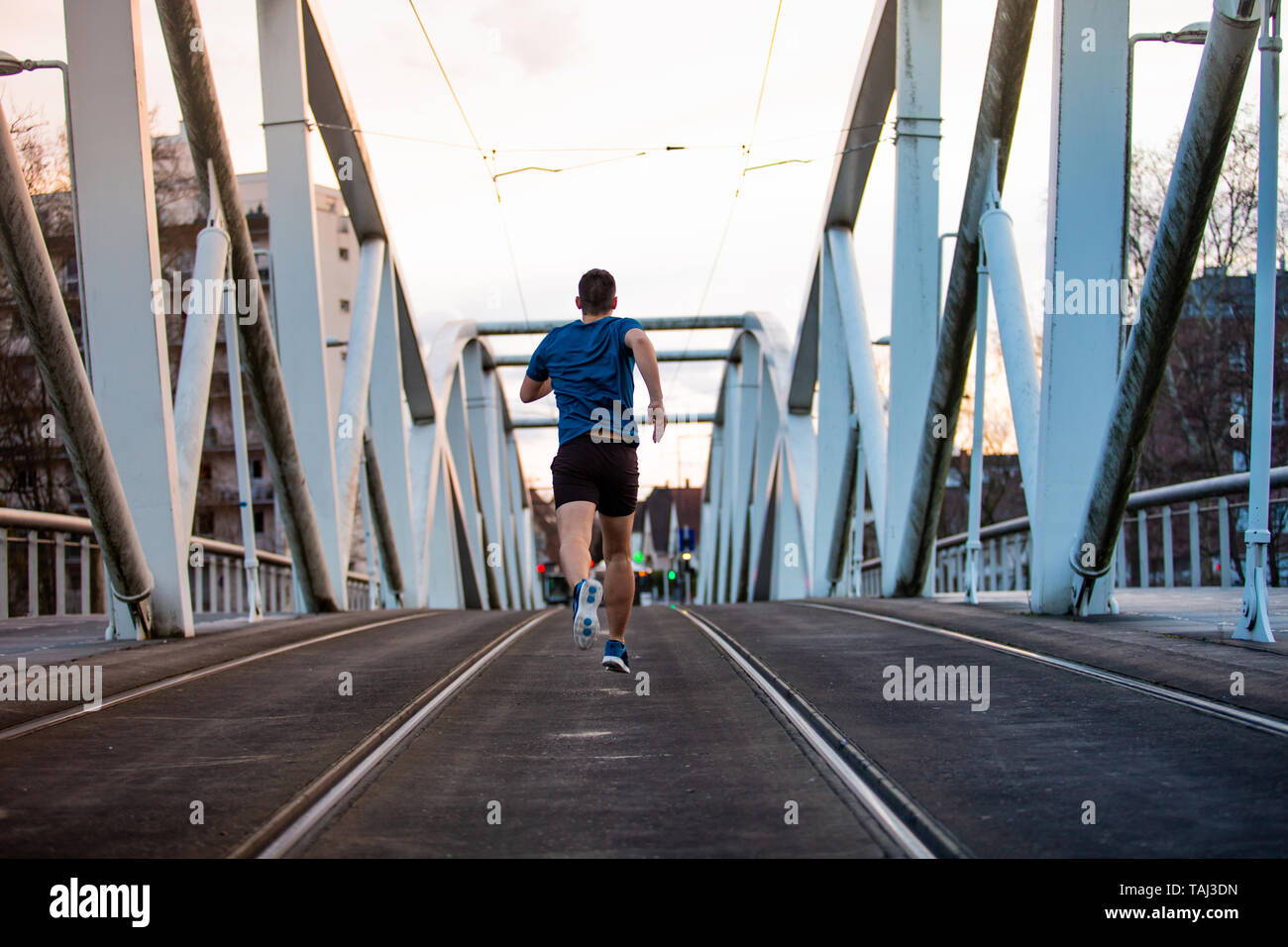Rear view Male runner running in a city park over bridge training for ...