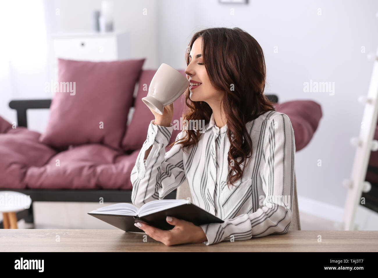 Beautiful young woman drinking coffee while reading book at home Stock ...
