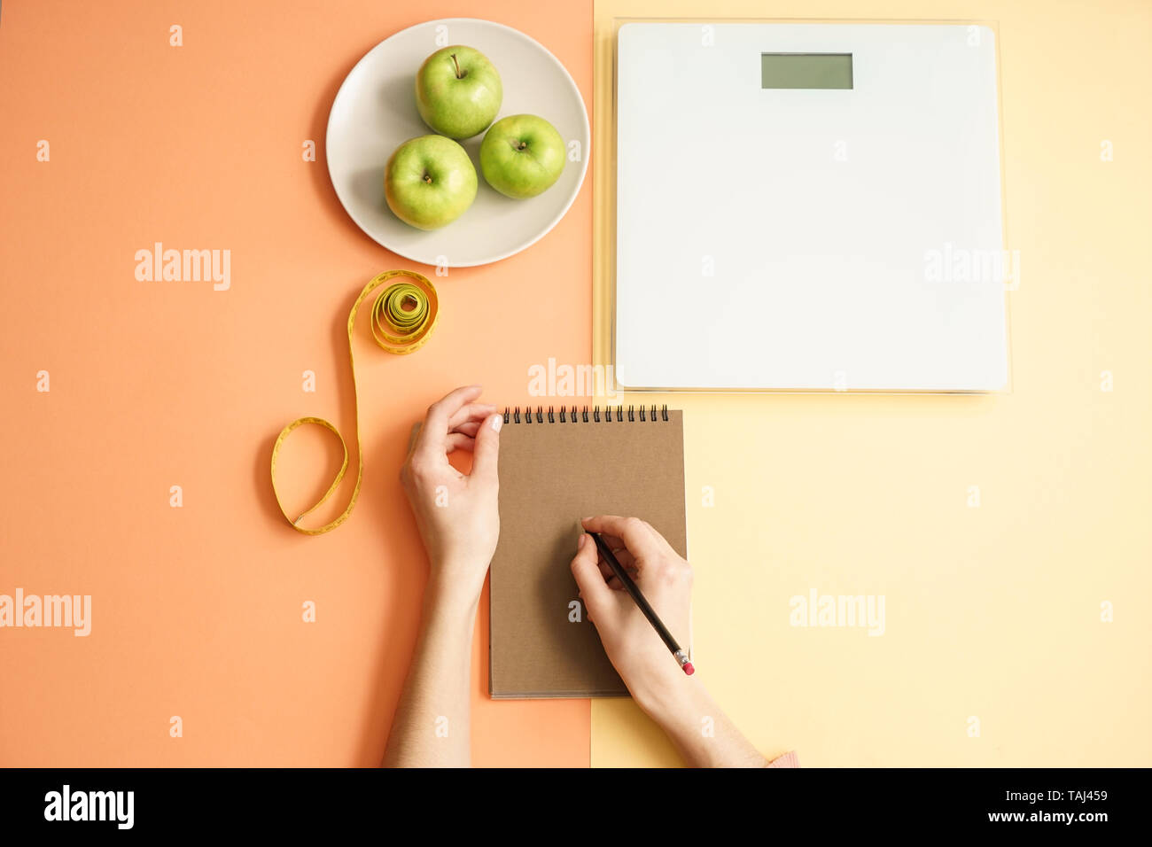 Woman writing in notebook, scales, apples and measuring tape on color ...
