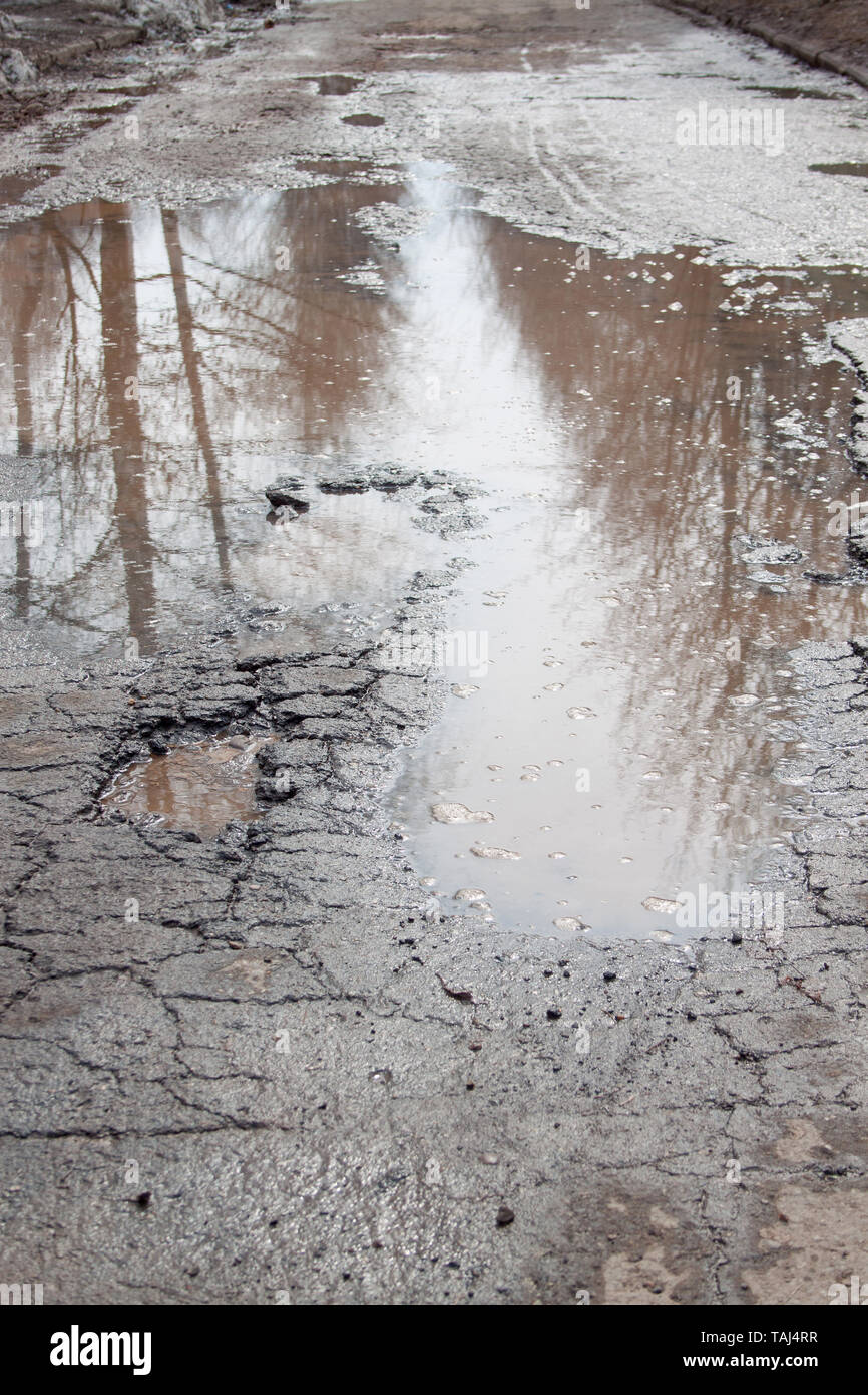 The bad asphalted road with a pothole filled with water. Dangerous ...