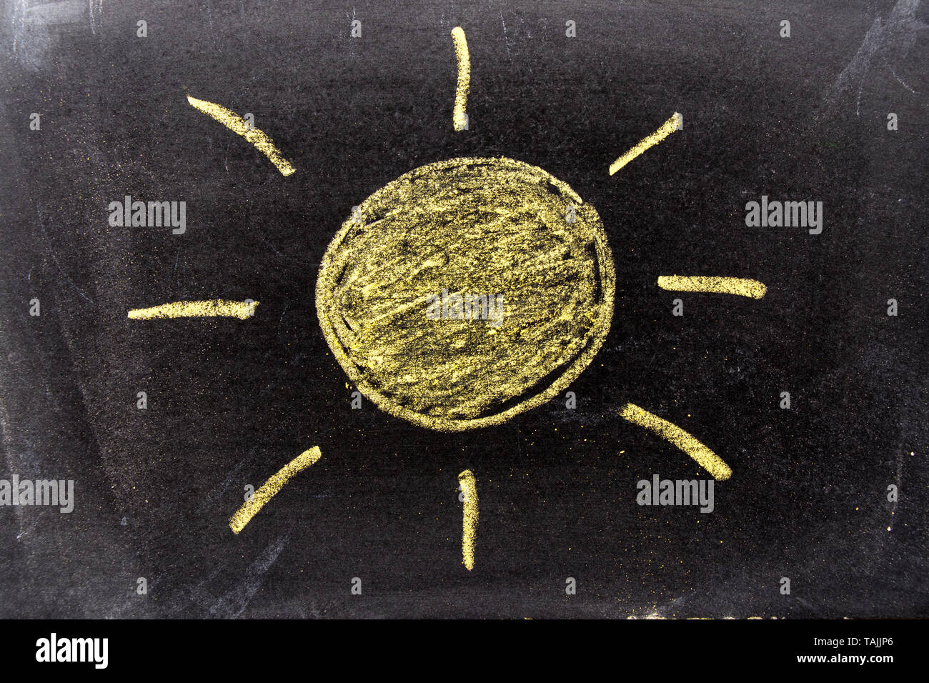 Yellow color chak hand drawing in sun with ray shape on blackboard ...