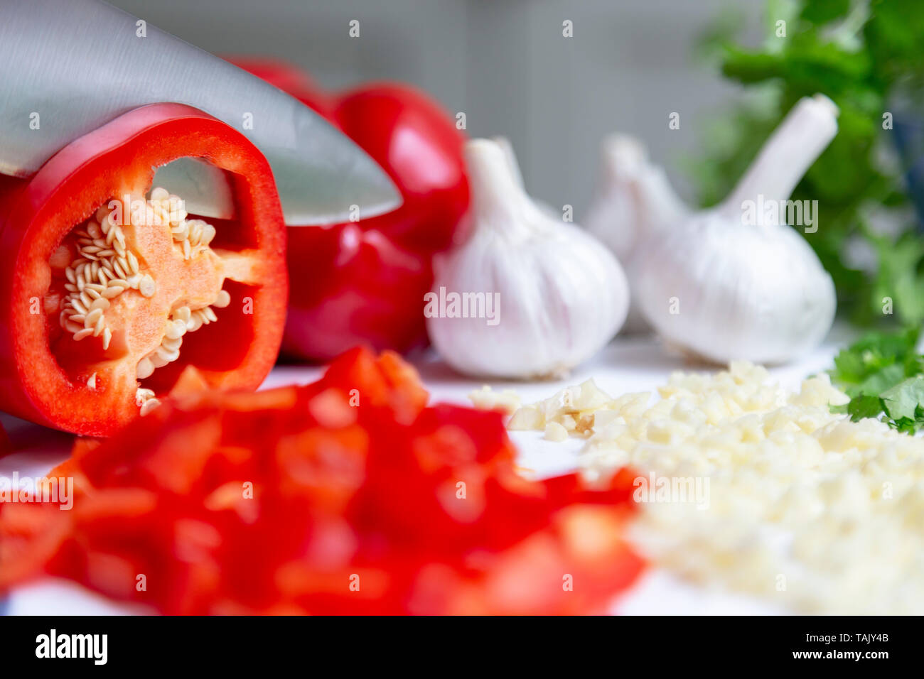 Knife cutting sweet red pepper with garlic bulbs and coriander Stock ...