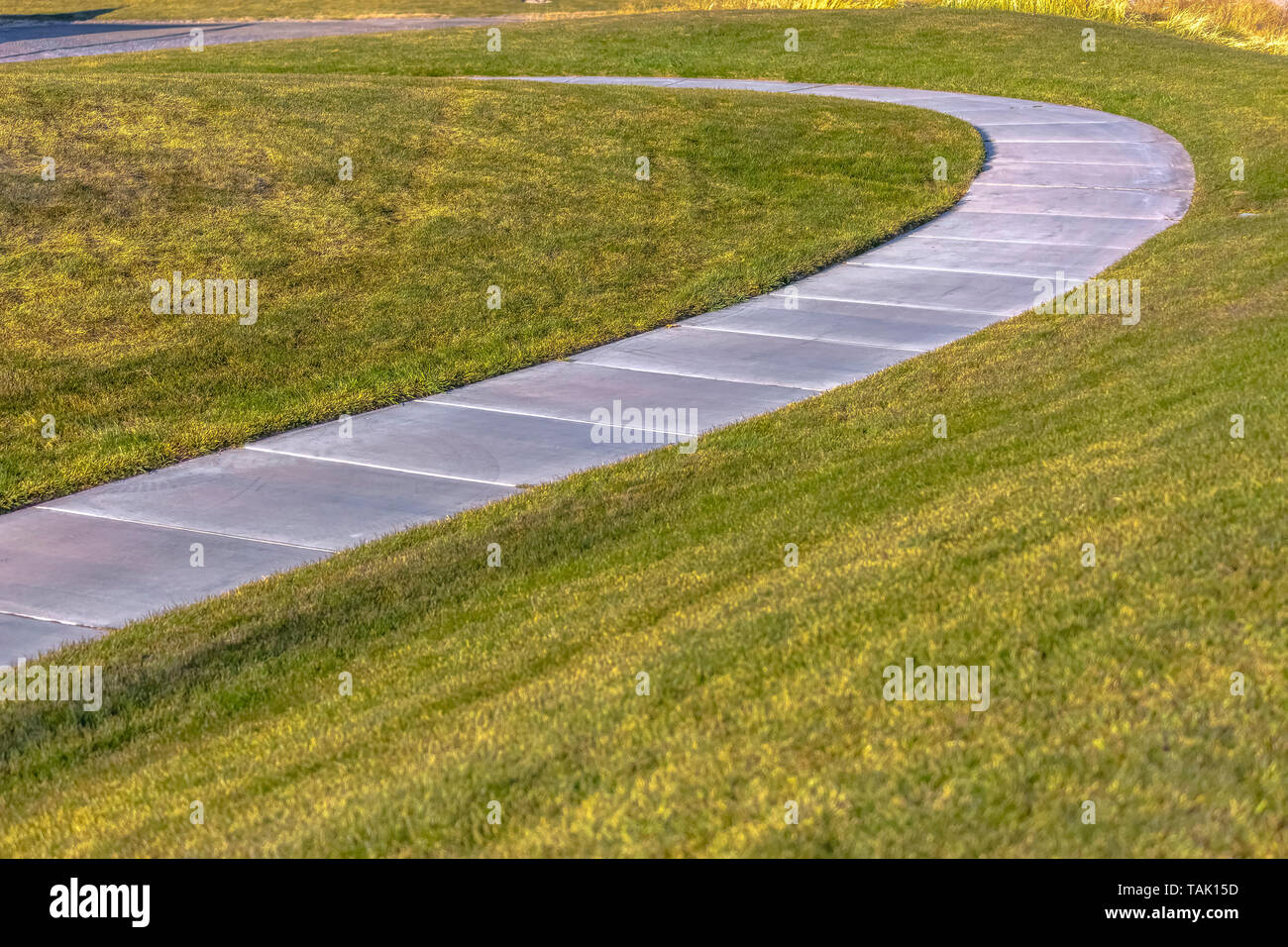 Paved footpath that curves through the grassy terrain viewed on a sunny ...