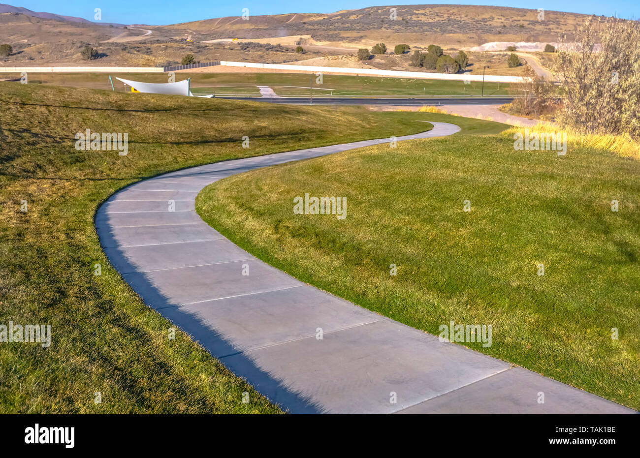 Pathway curving through a lush grassy terrain lit by sunlight on a ...