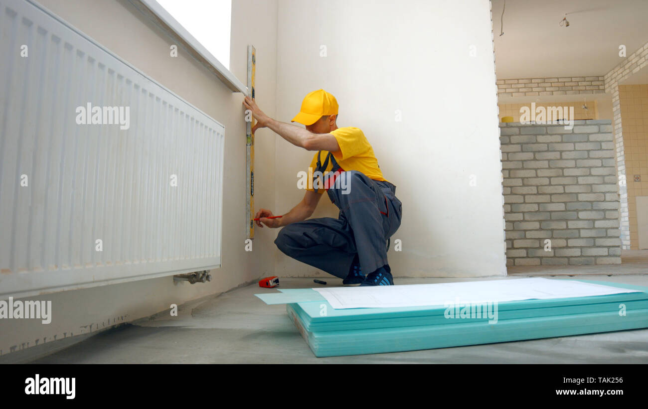 Builder in yellow uniform working indoors. Male builder measuring a ...