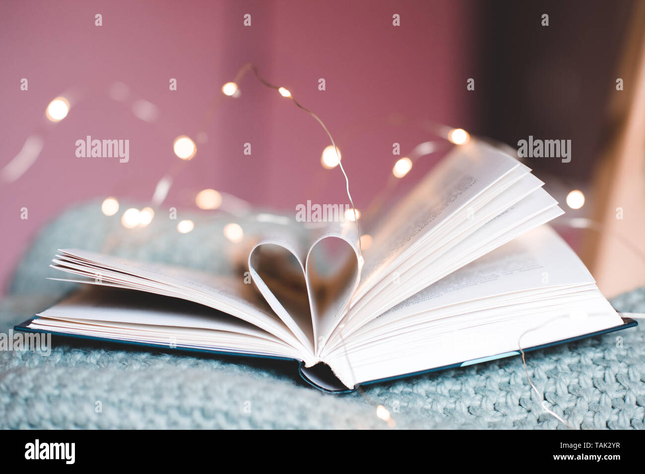Open book with folded sheets in heart shape closeup over lights. Love ...