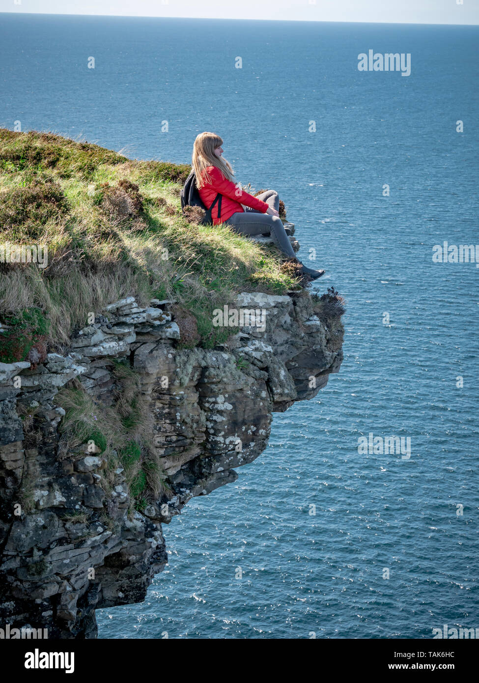 Young woman sitting on the edge of a cliff at the Irish west coast ...