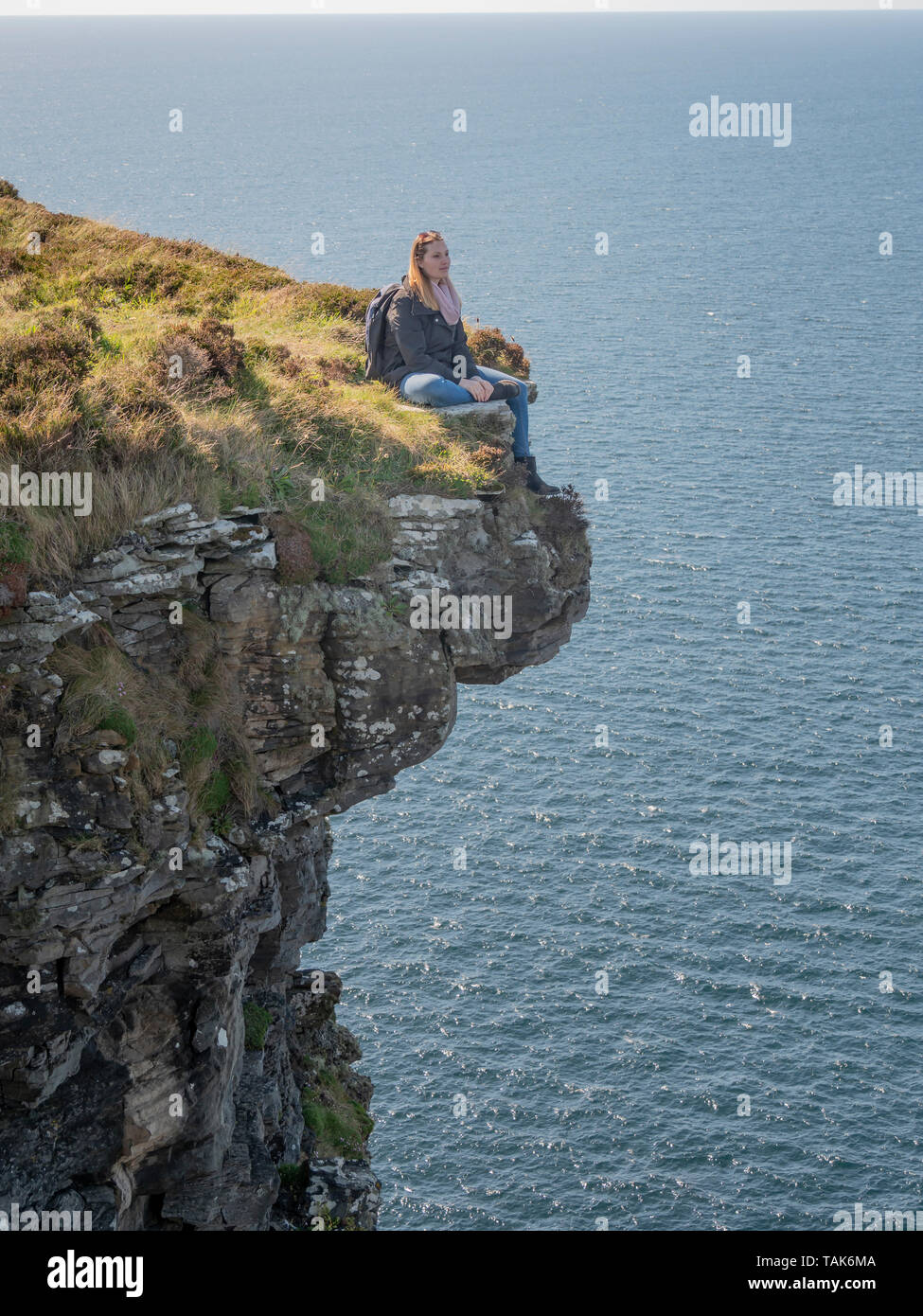 Young woman sitting on the edge of a cliff at the Irish west coast ...