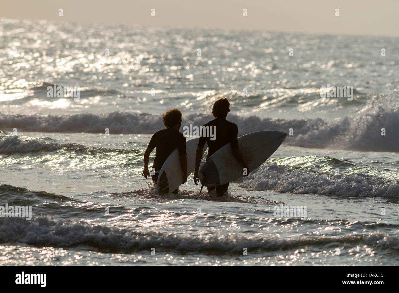 two young surfers holding their surfboards and getting into the sea ...