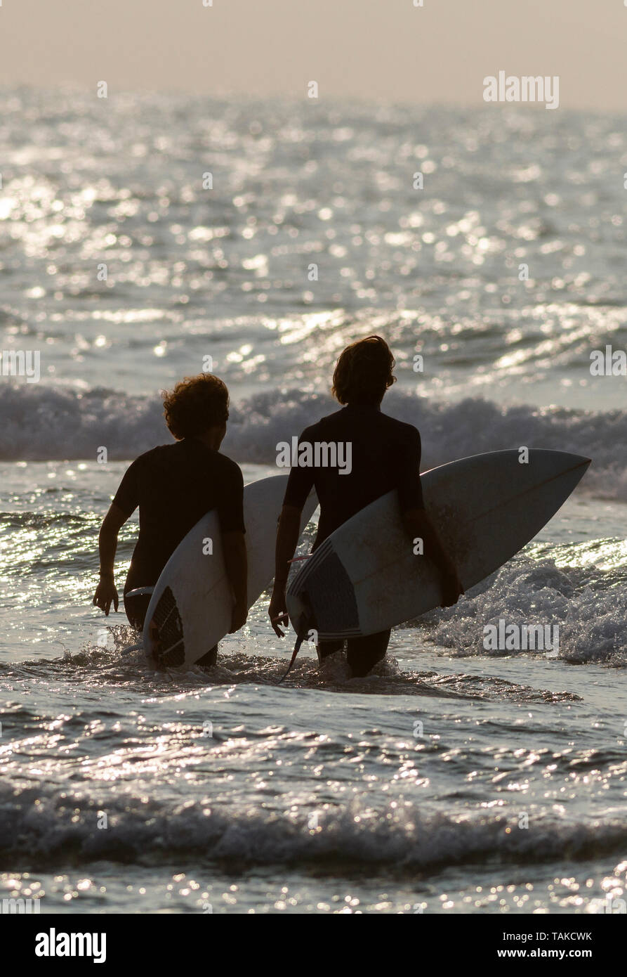 two young surfers holding their surfboards and getting into the sea ...