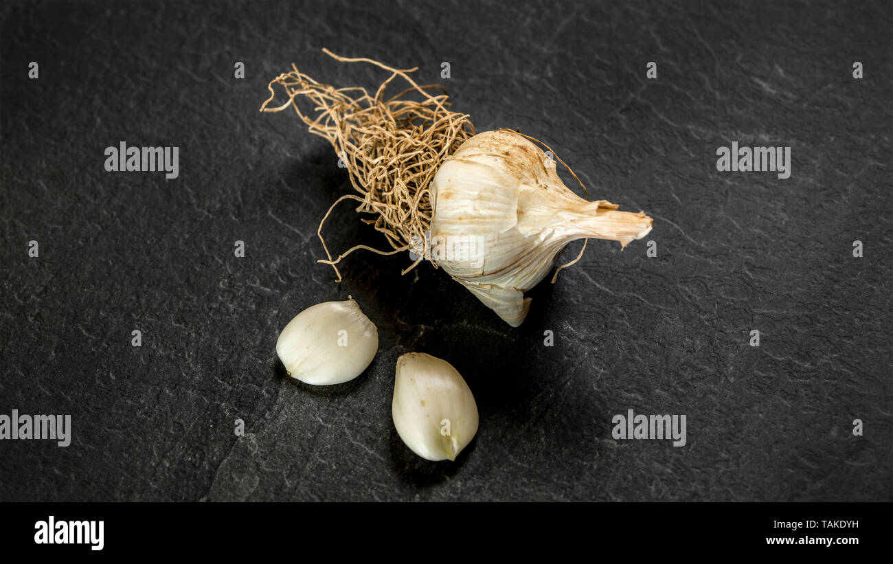 Small garlic bulb with roots, two cloves next on black working board ...