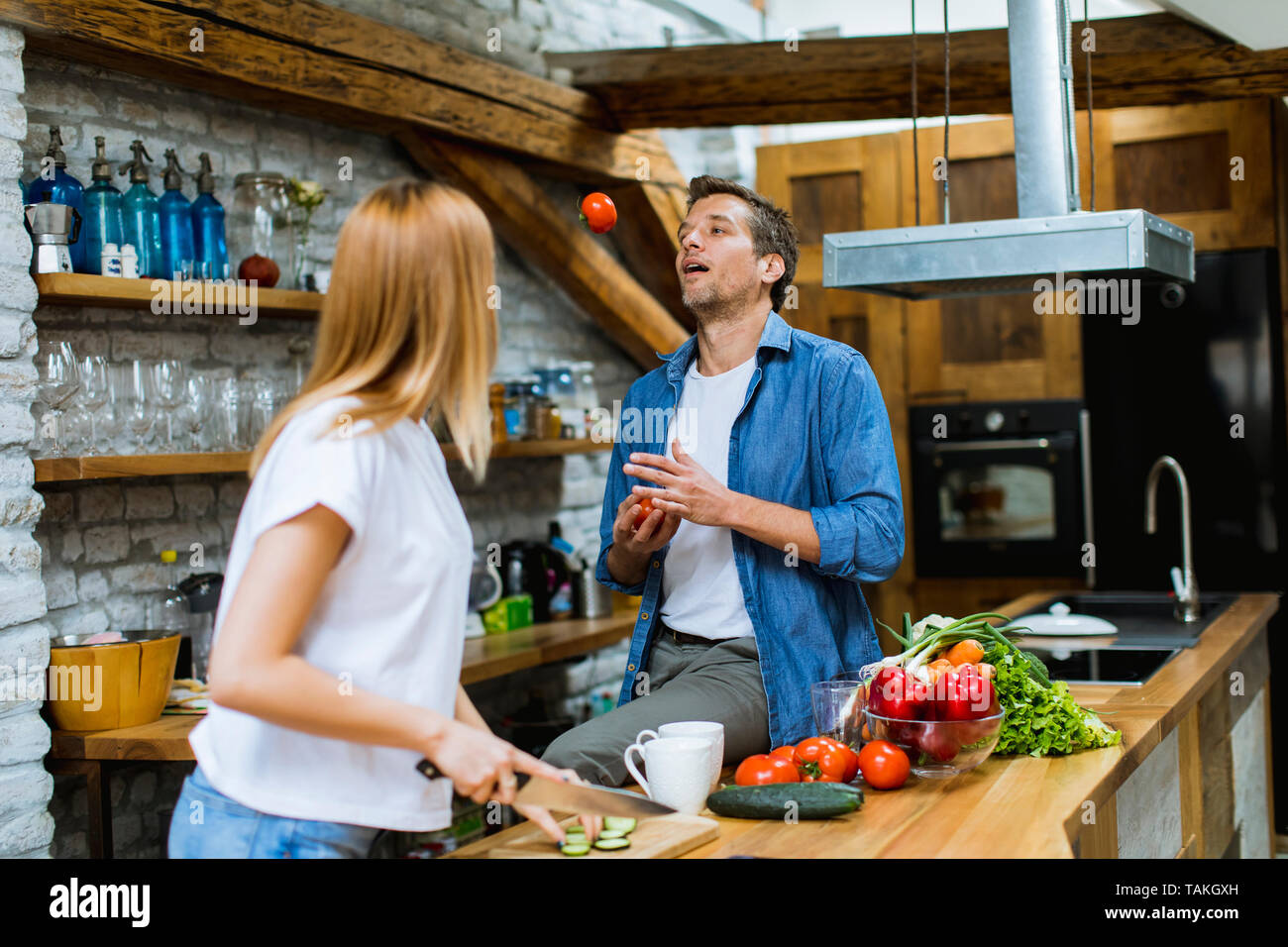Lovely cheerful young couple cooking dinner together and having fun at ...