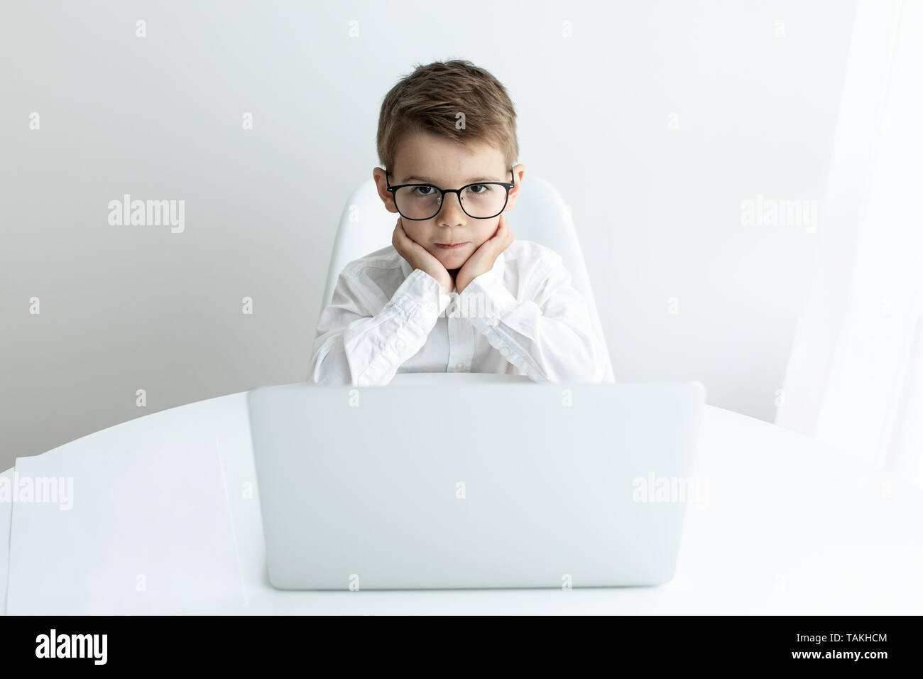 Cute little boy using laptop while doing homework against white ...