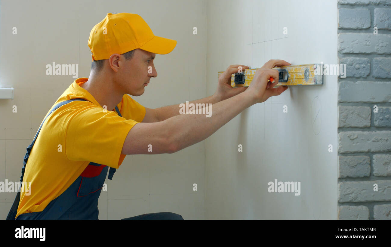 Caucasian builder measuring wall with level tool. Young repairman ...