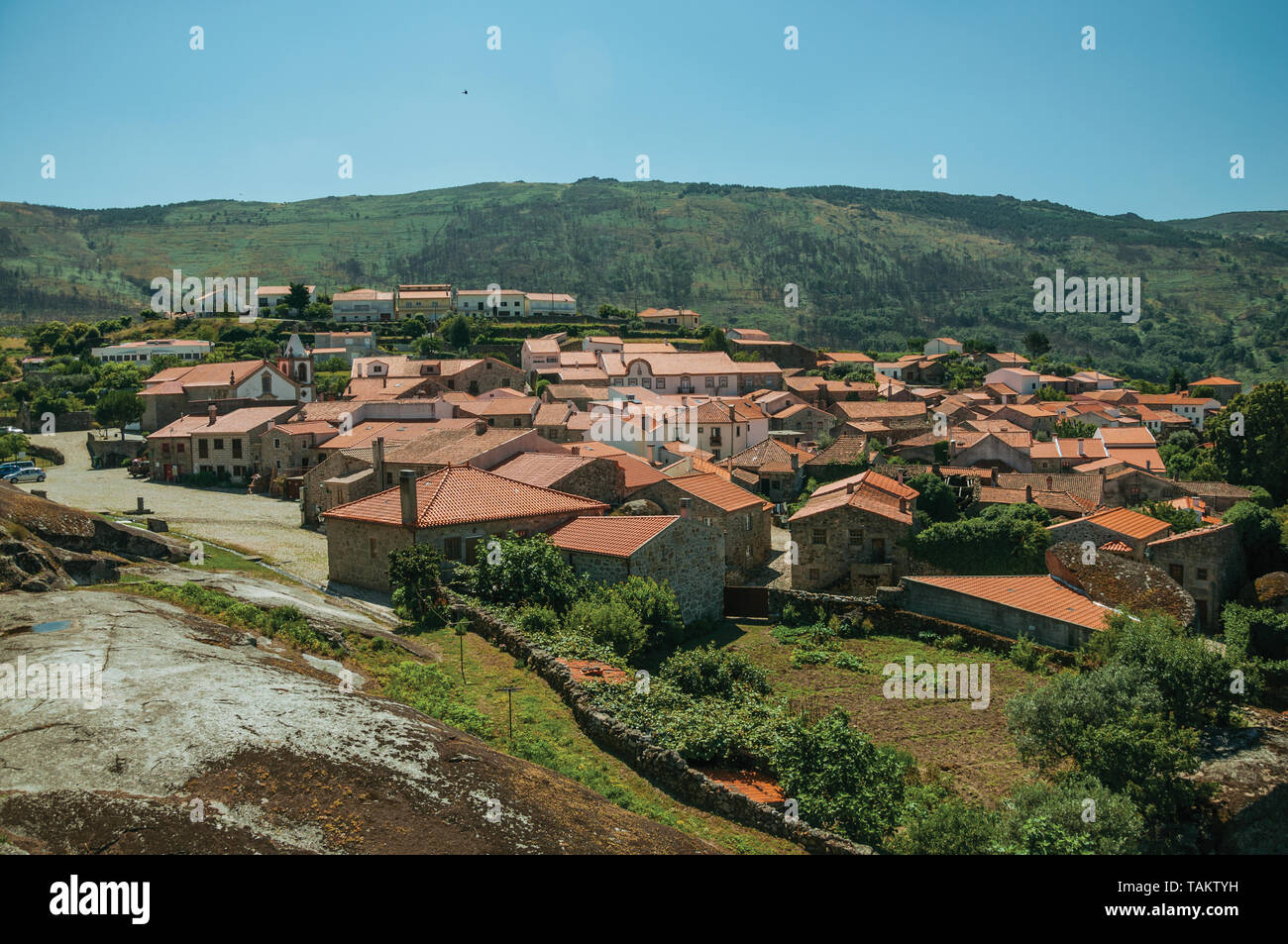 Hilly landscape covered by trees and rocks with the roofs of Linhares ...