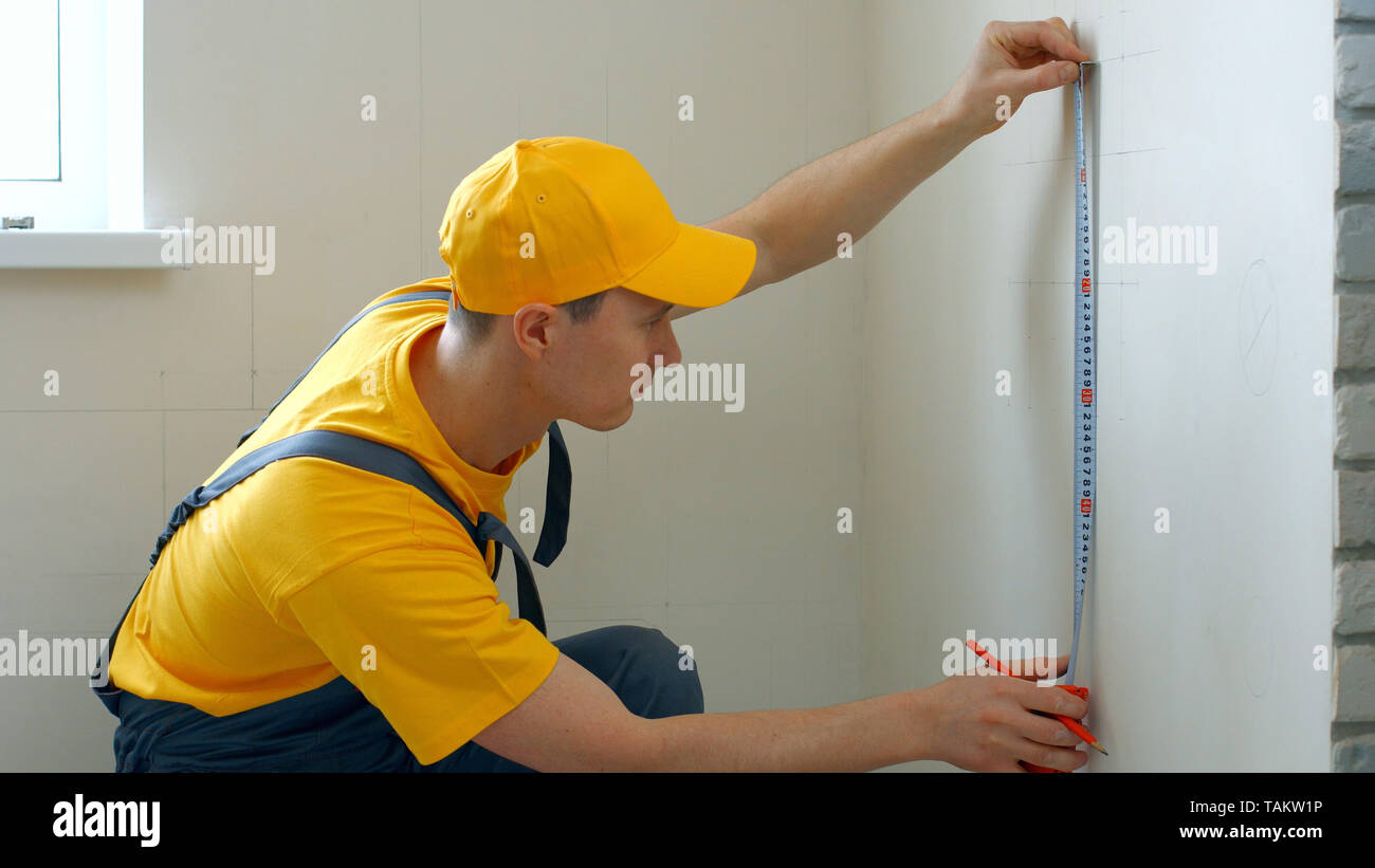 Young caucasian builder measuring wall with measuring tape ...