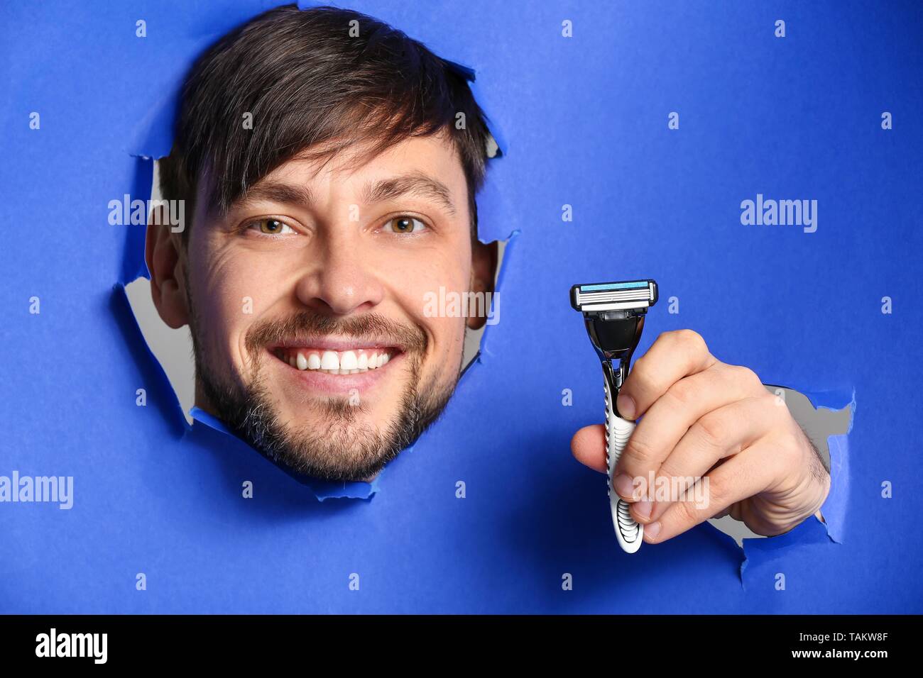 Handsome man with razor visible through holes in torn color paper Stock ...