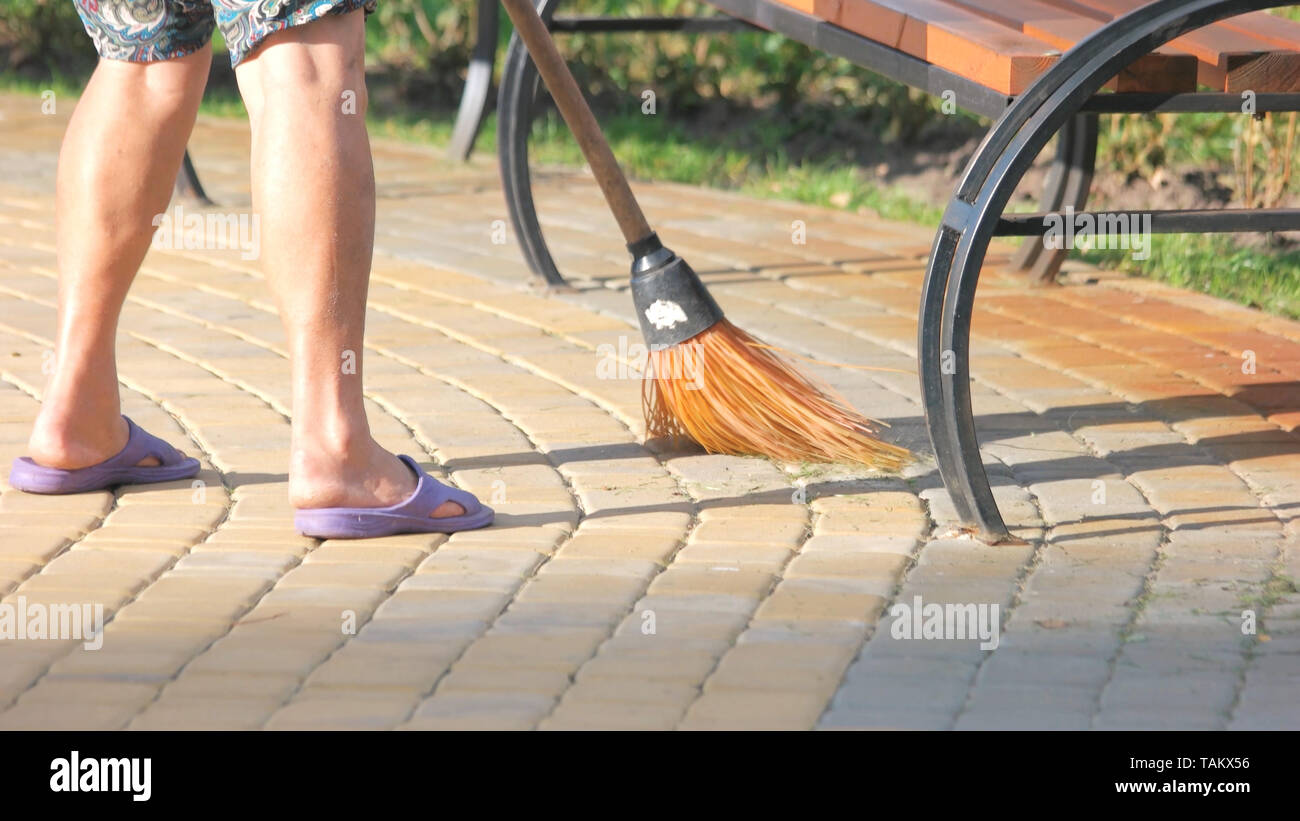 Workers is sweeping leaves outdoors. Broom cleans paving slabs on sunny ...
