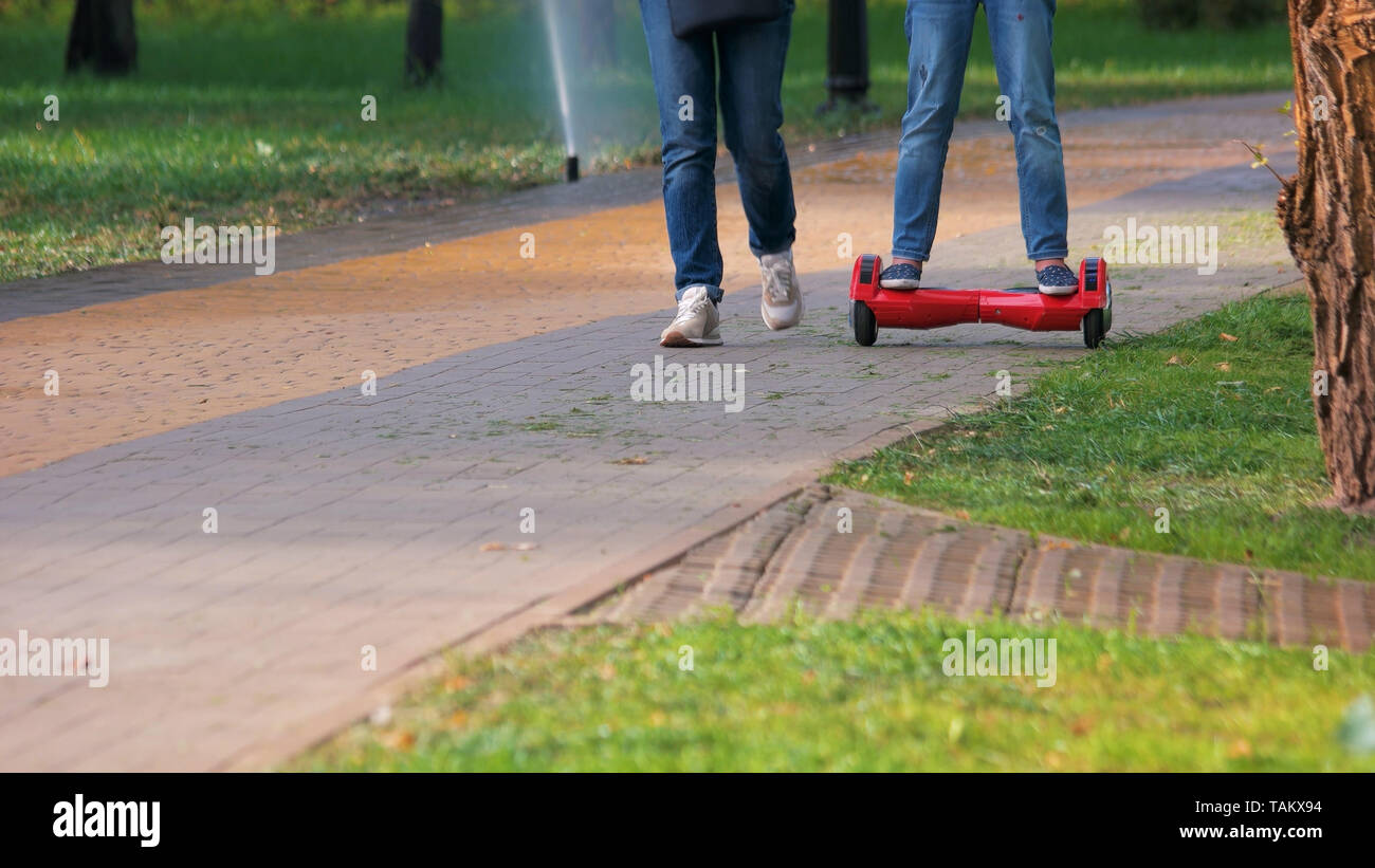 Girls legs on hover board in summer park. People walking outdoors ...