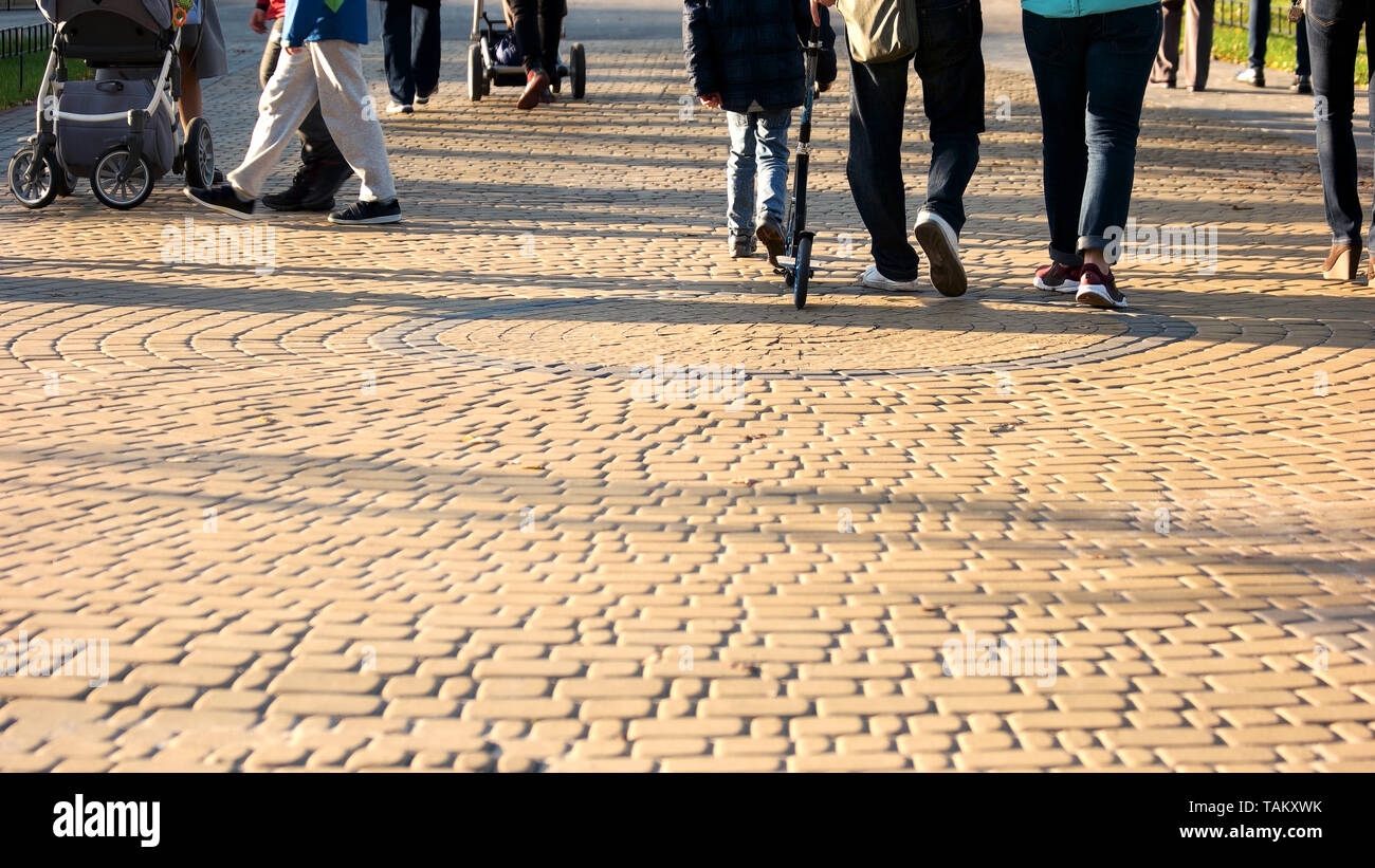 Crowd of people are walking in the park. Cubblestone pavement surface ...
