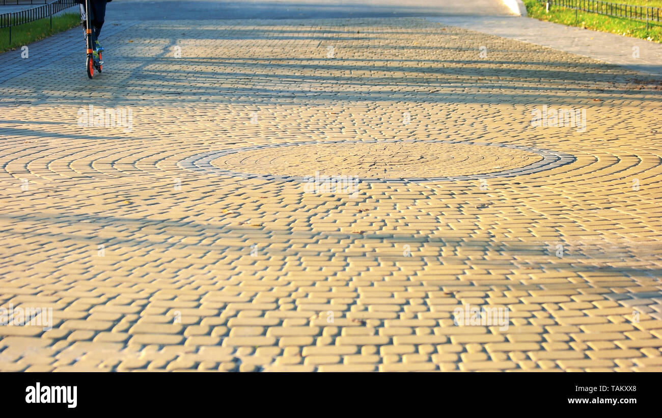Cobblestone pavement in city park, down view. Low section boy riding on ...