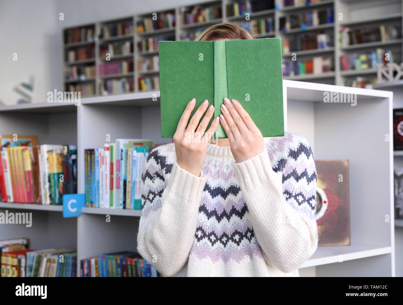 Young woman hiding face behind book in library Stock Photo - Alamy