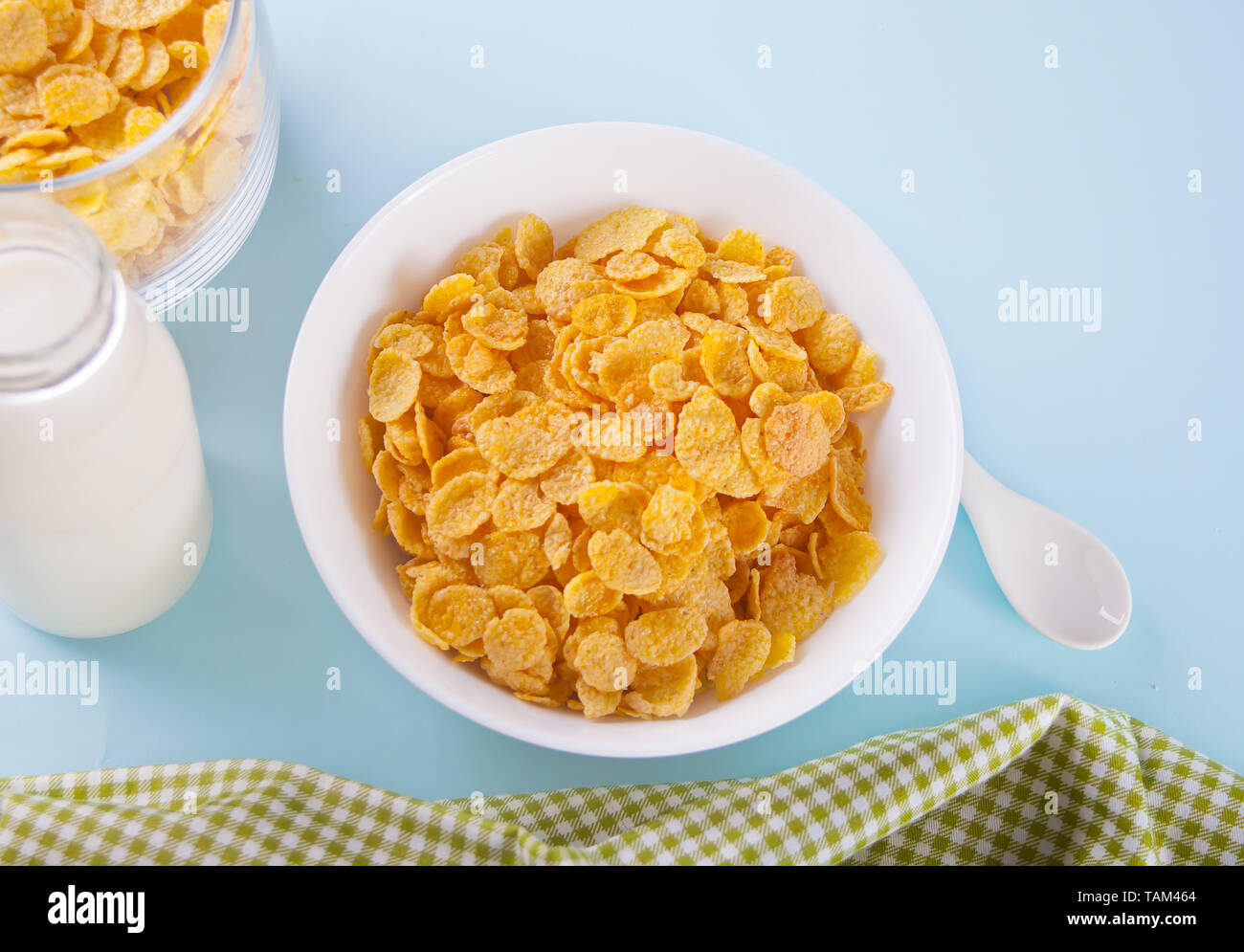 A bowl of dry corn flakes cereal and a bottle of milk on the blue table ...