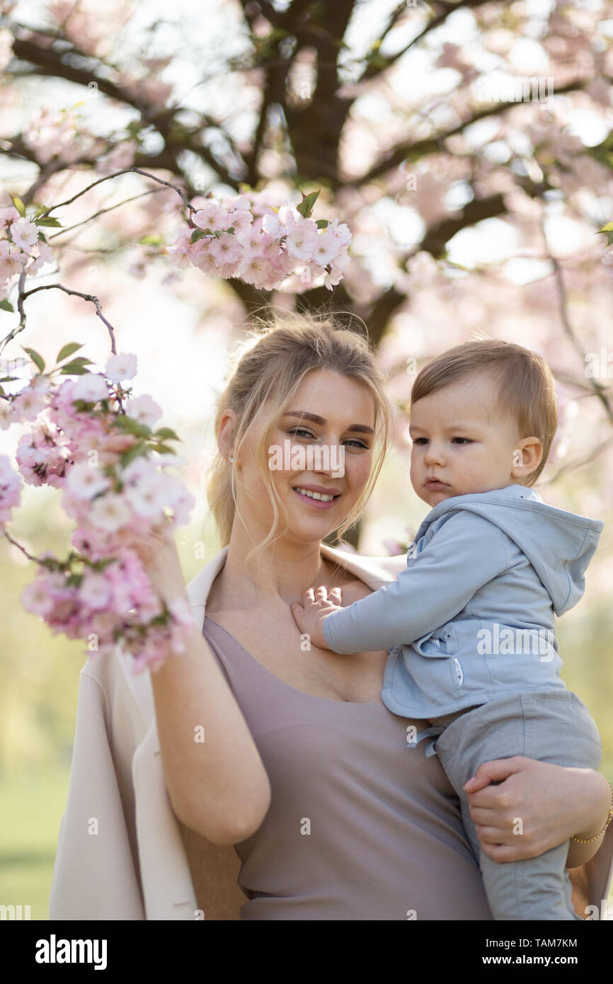 Young mother mom holding her little baby son boy child under blossoming ...