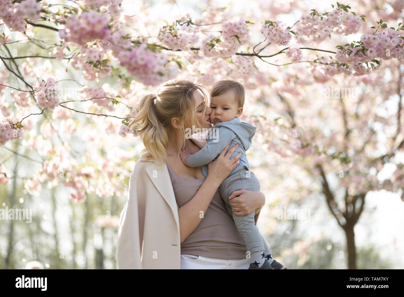 Young mother mom holding her little baby son boy child under blossoming ...
