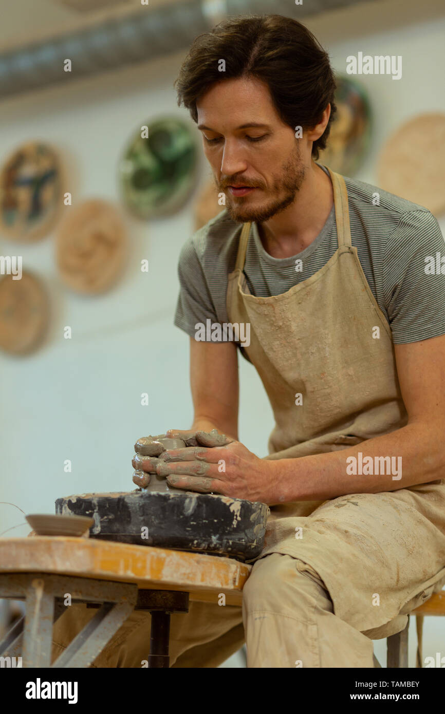 Moving clay figure. Resolute calm master sitting in equipped workshop ...