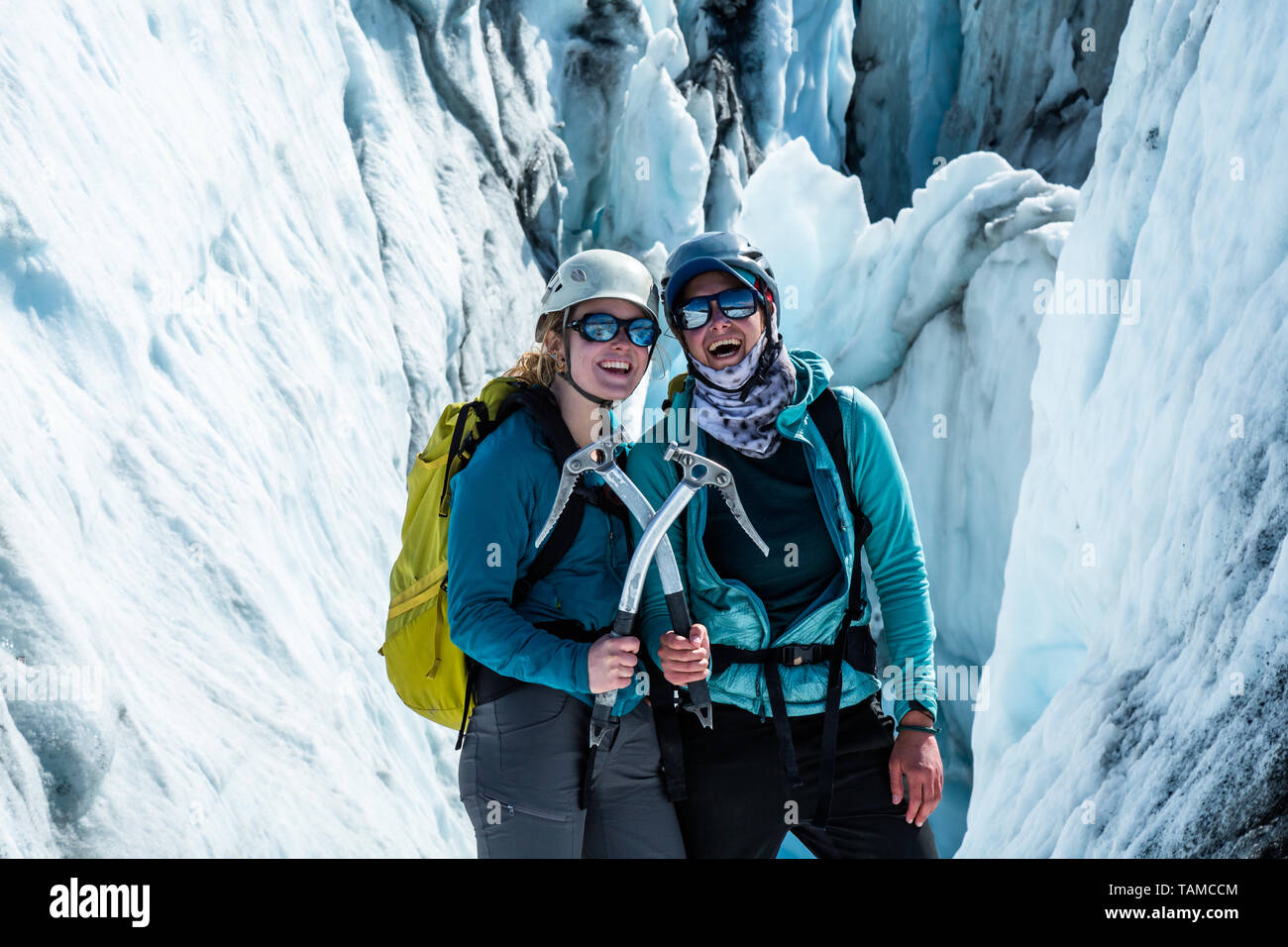 Two women with crossed ice axes stand in front of a large open crevasse ...