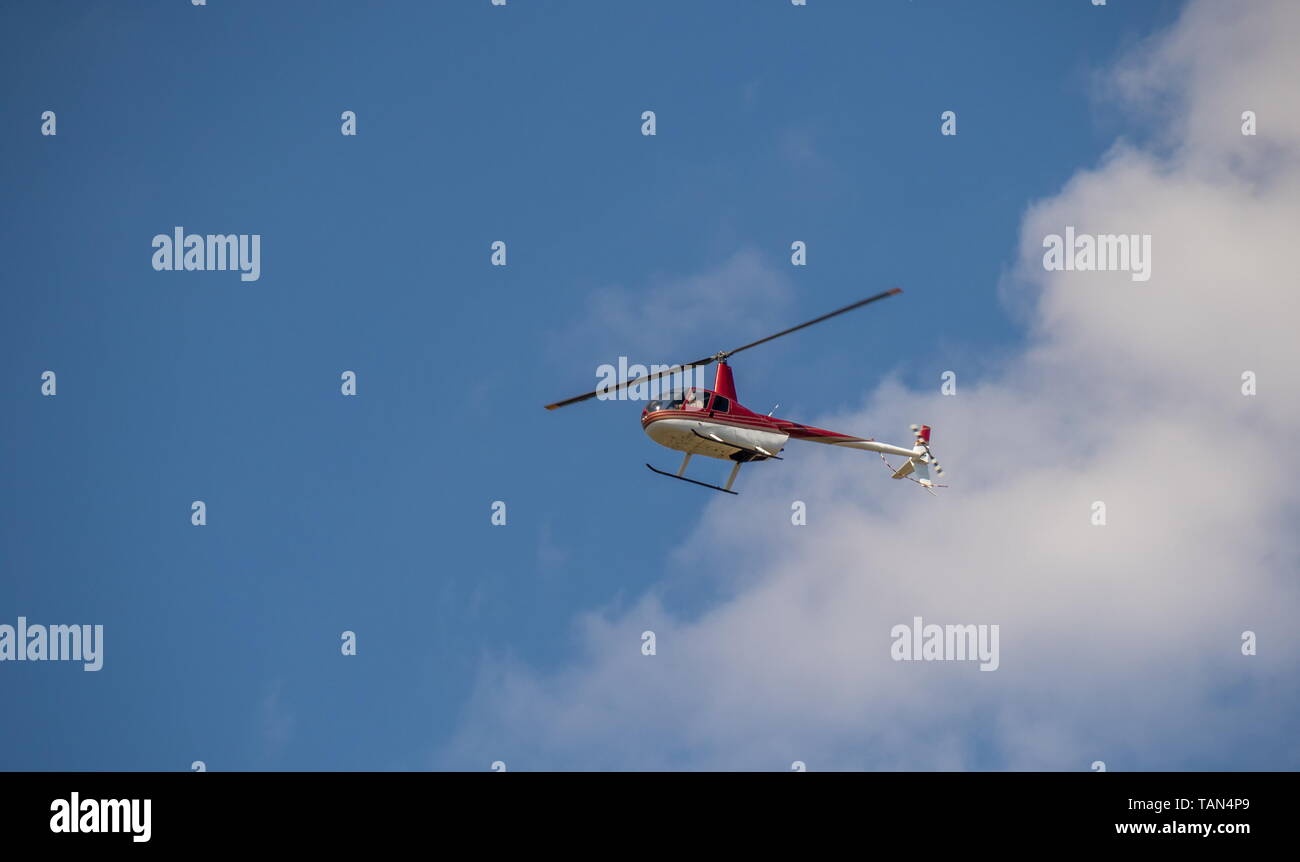 A red and white helicopter flies through a white cloud in a blue sky ...
