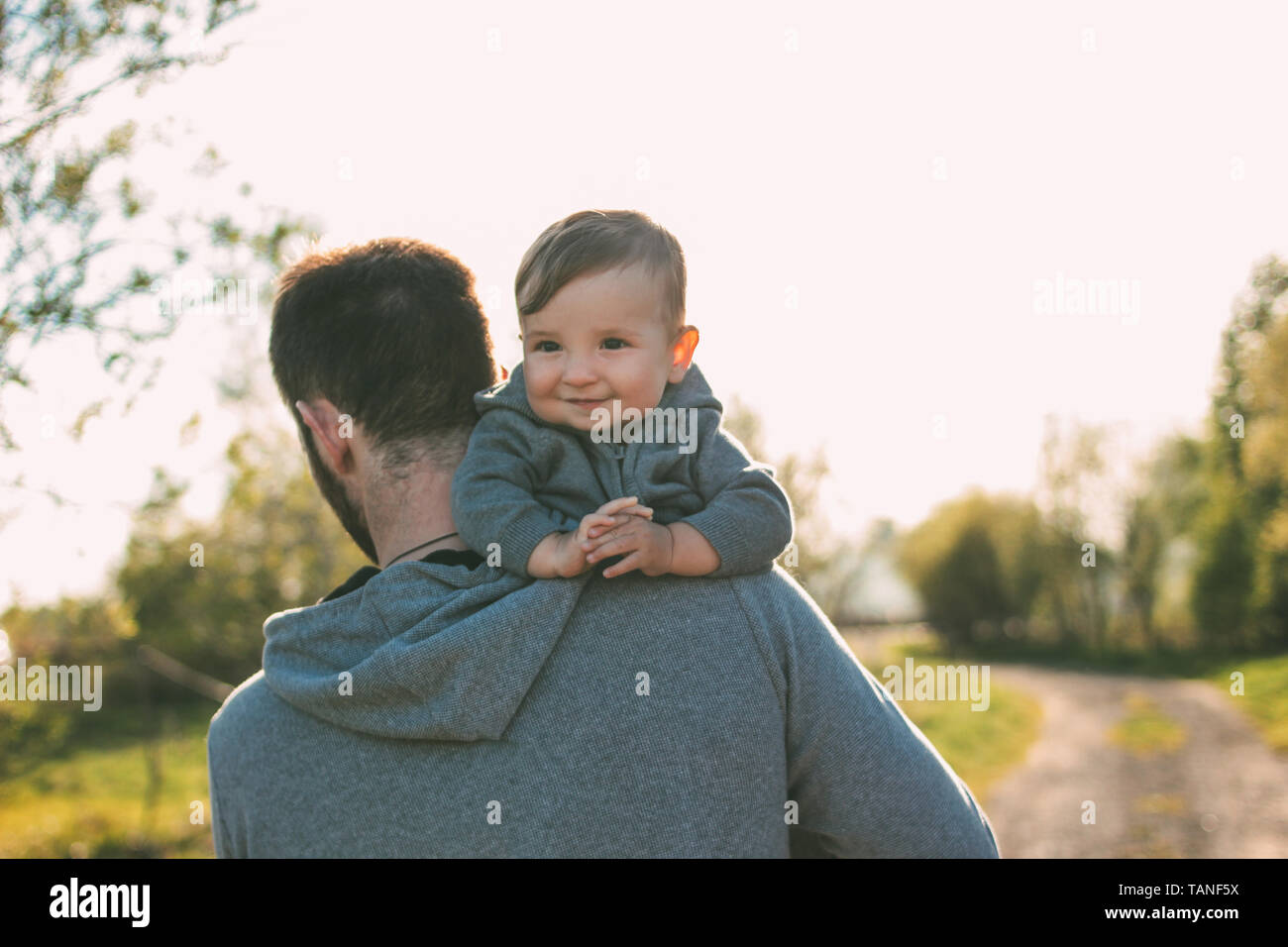 Cute baby boy on his dad's shoulders walking on road outdoors ...