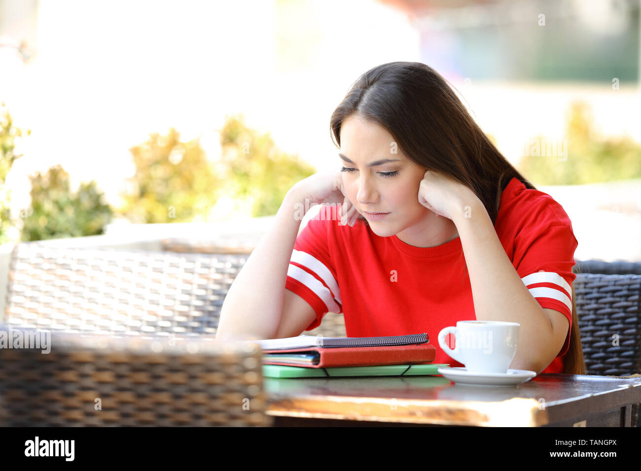 Serious student in red studying reading notes sitting in a coffee shop ...