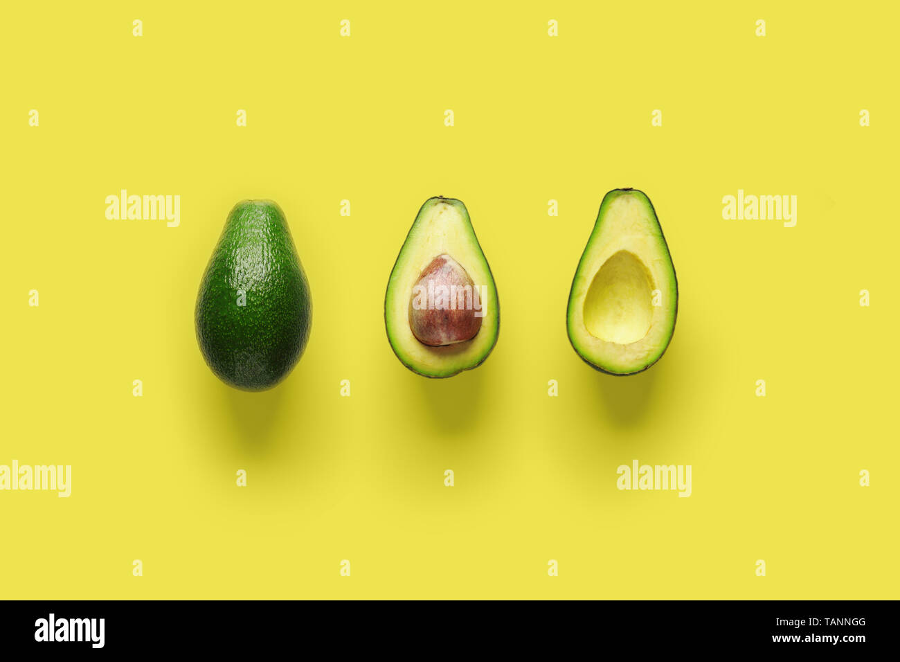 Whole avocado fruit and two halves in a row isolated on yellow ...