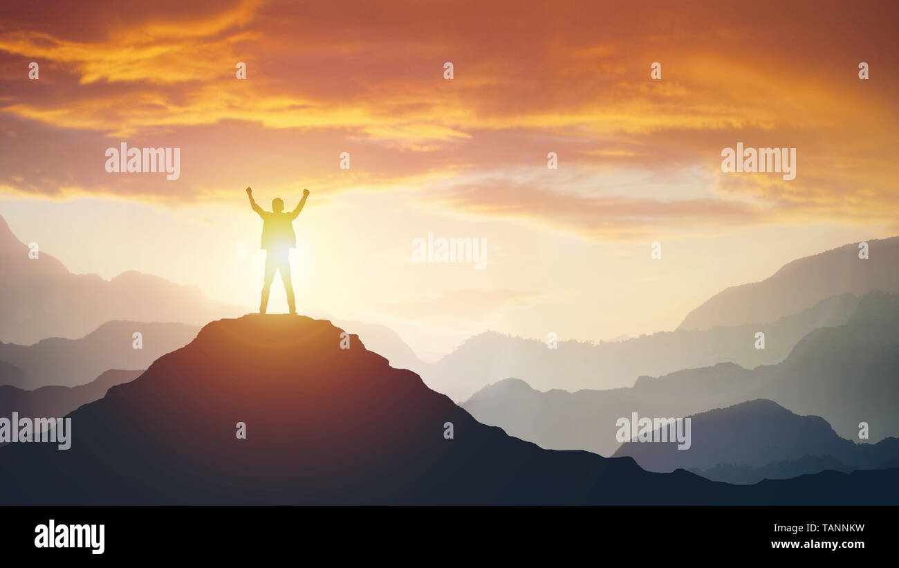 Man standing on edge of mountain feeling victorious with arms up in the ...
