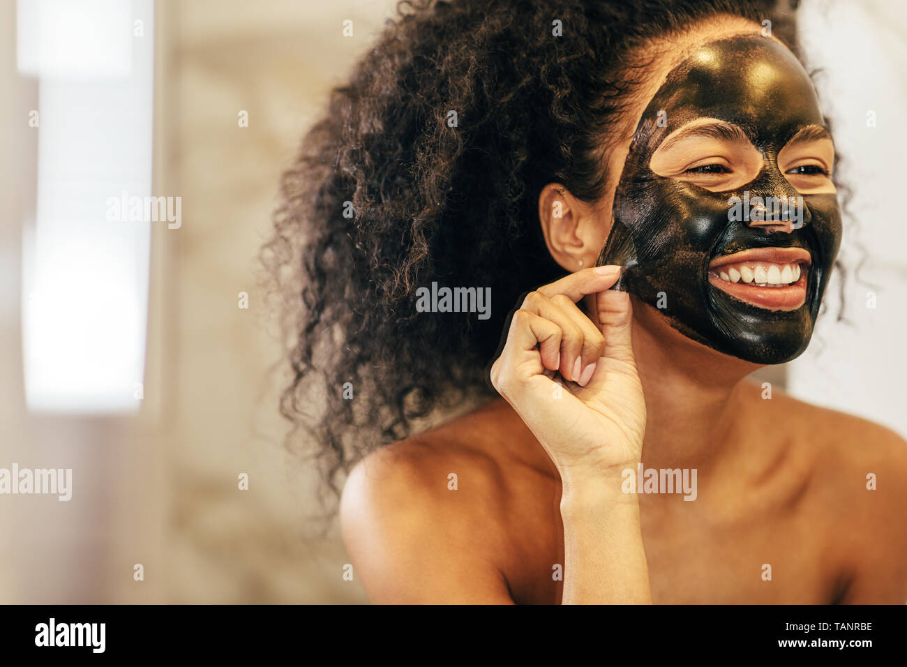 Smiling woman removing black cosmetic mask from her face Stock Photo ...