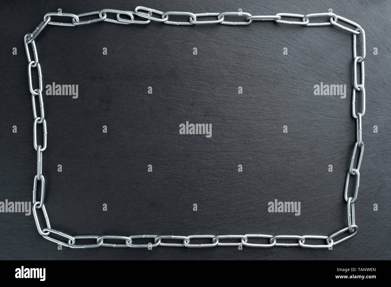 Frame made out of shiny metal chain on a dark stone slate plate ...
