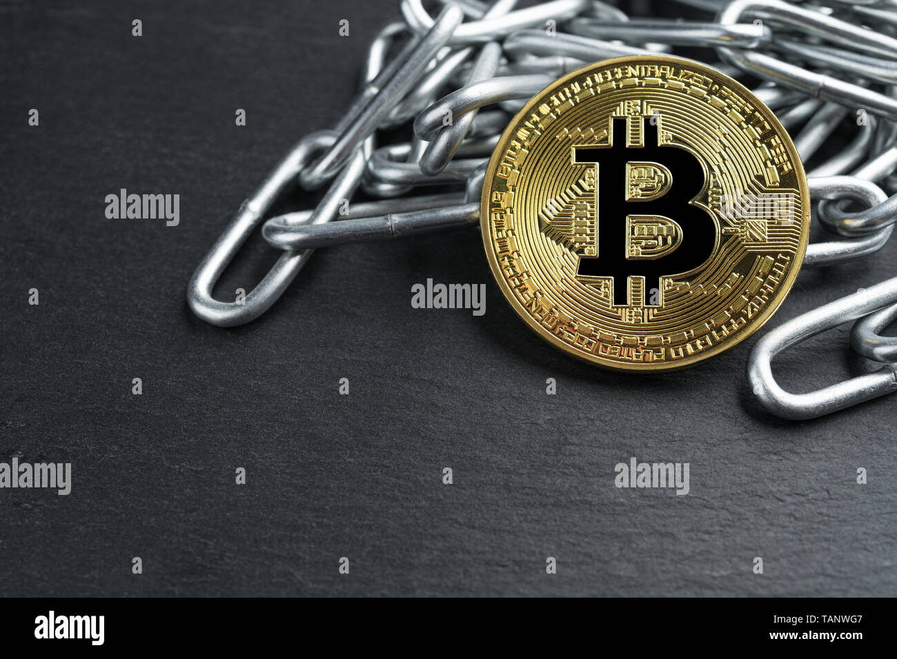 Physical Bitcoin gold coin on a convoluted shiny metal chain on dark ...